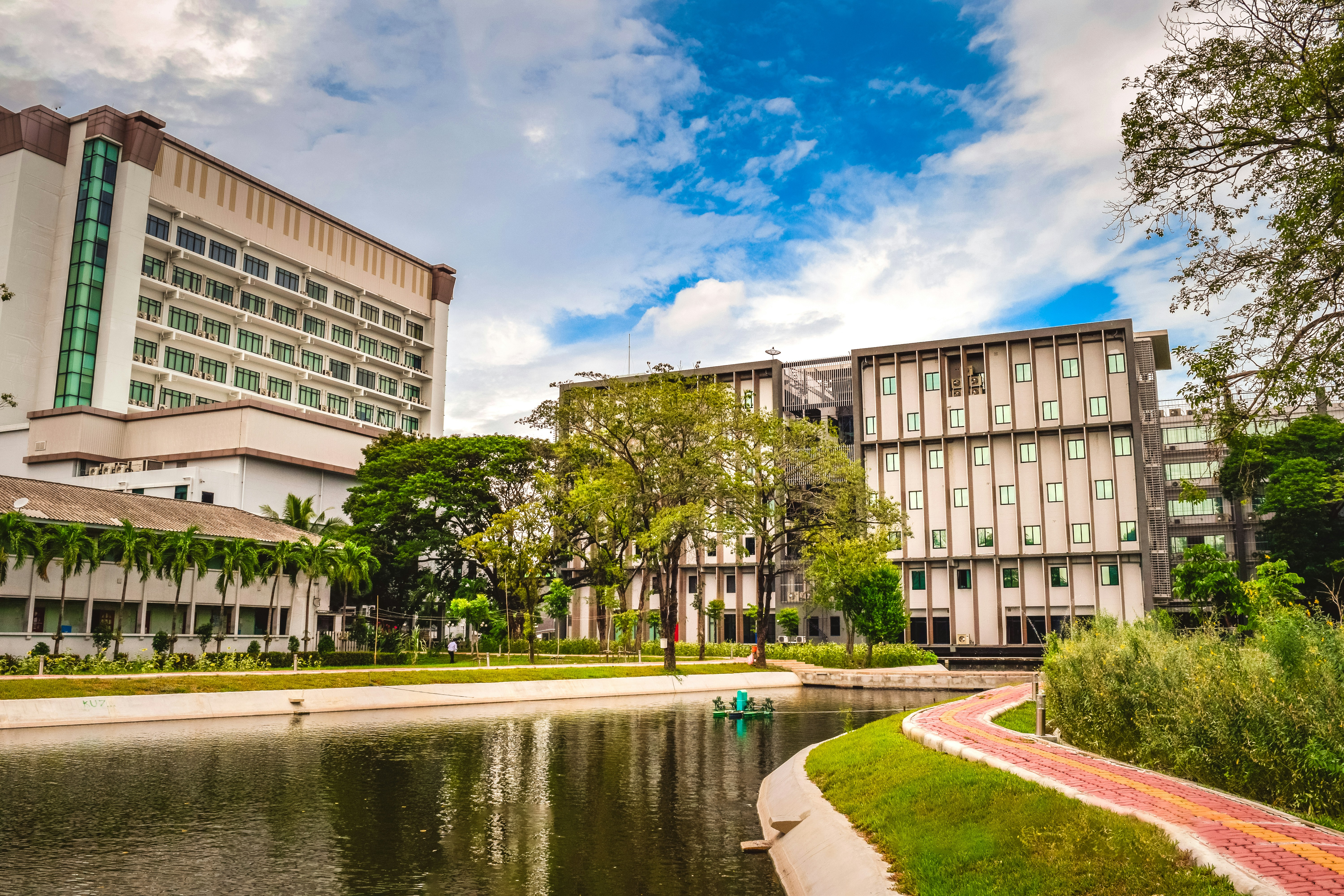 Contemporary buildings beside a serene pond under a vibrant blue sky.
