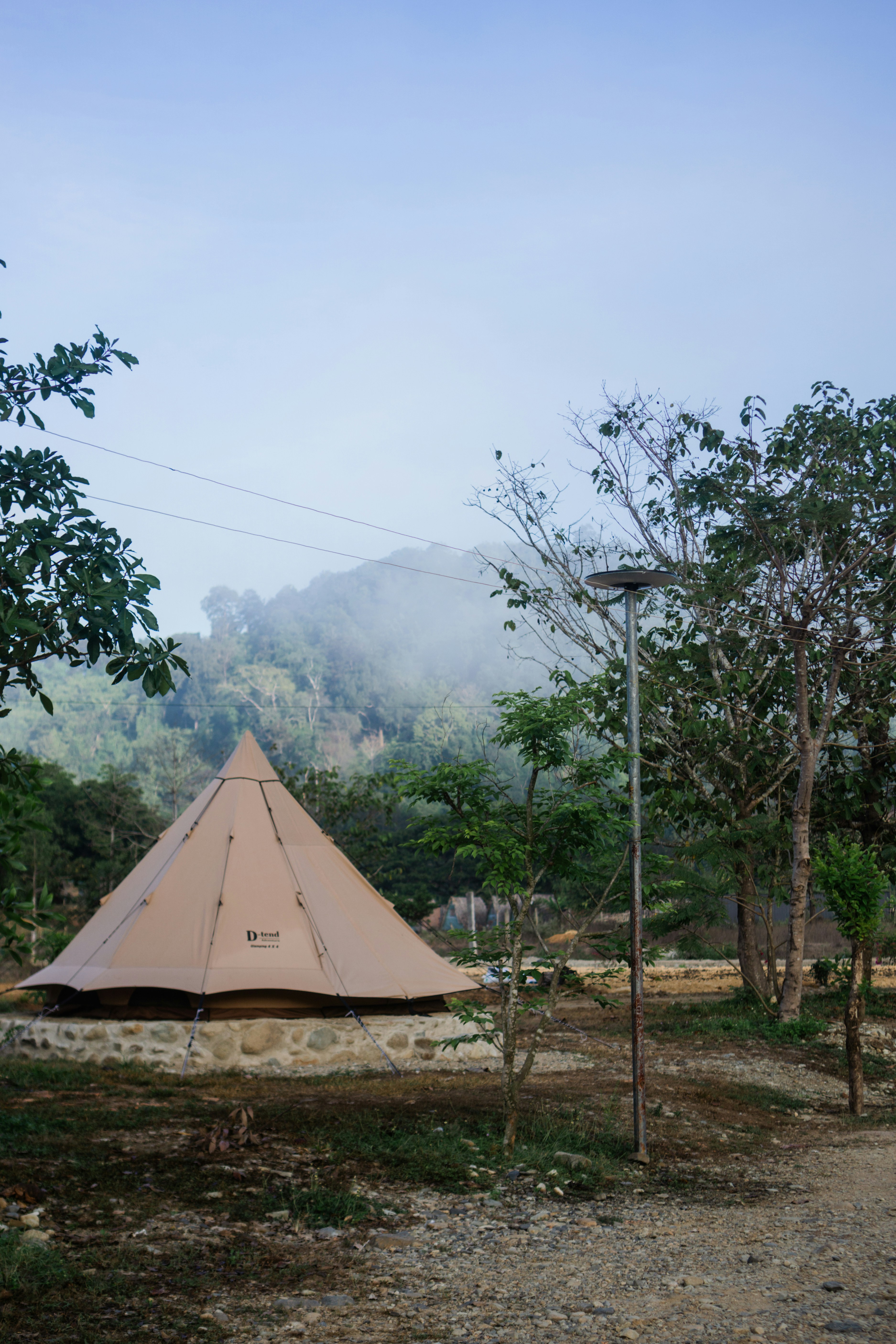 Beige Camping Tent Quietly Anchored Beneath Misty Hills and a Lone Lamp