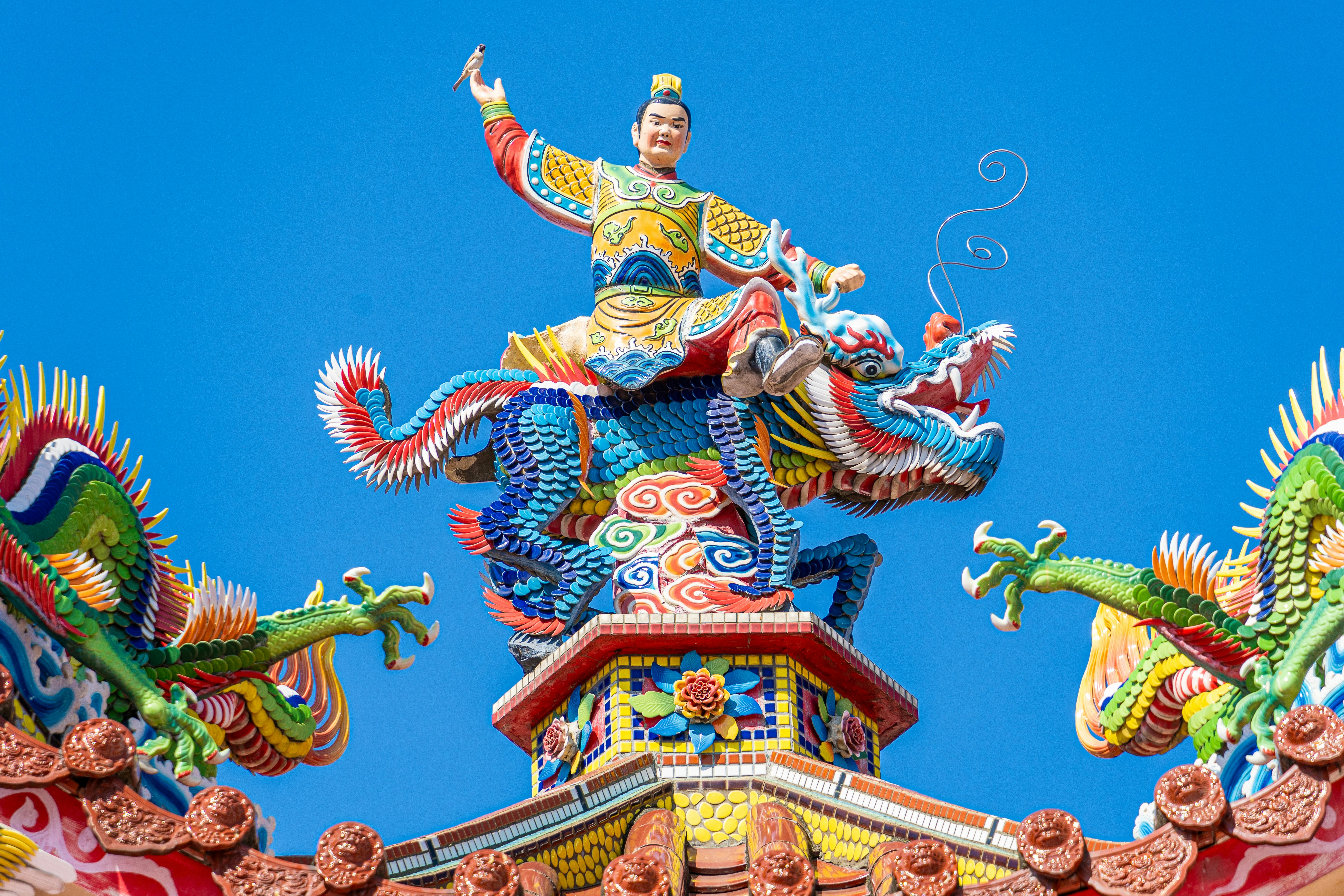 A vibrant sculpture depicting a deity riding a dragon, adorned with intricate colors against a clear blue sky.