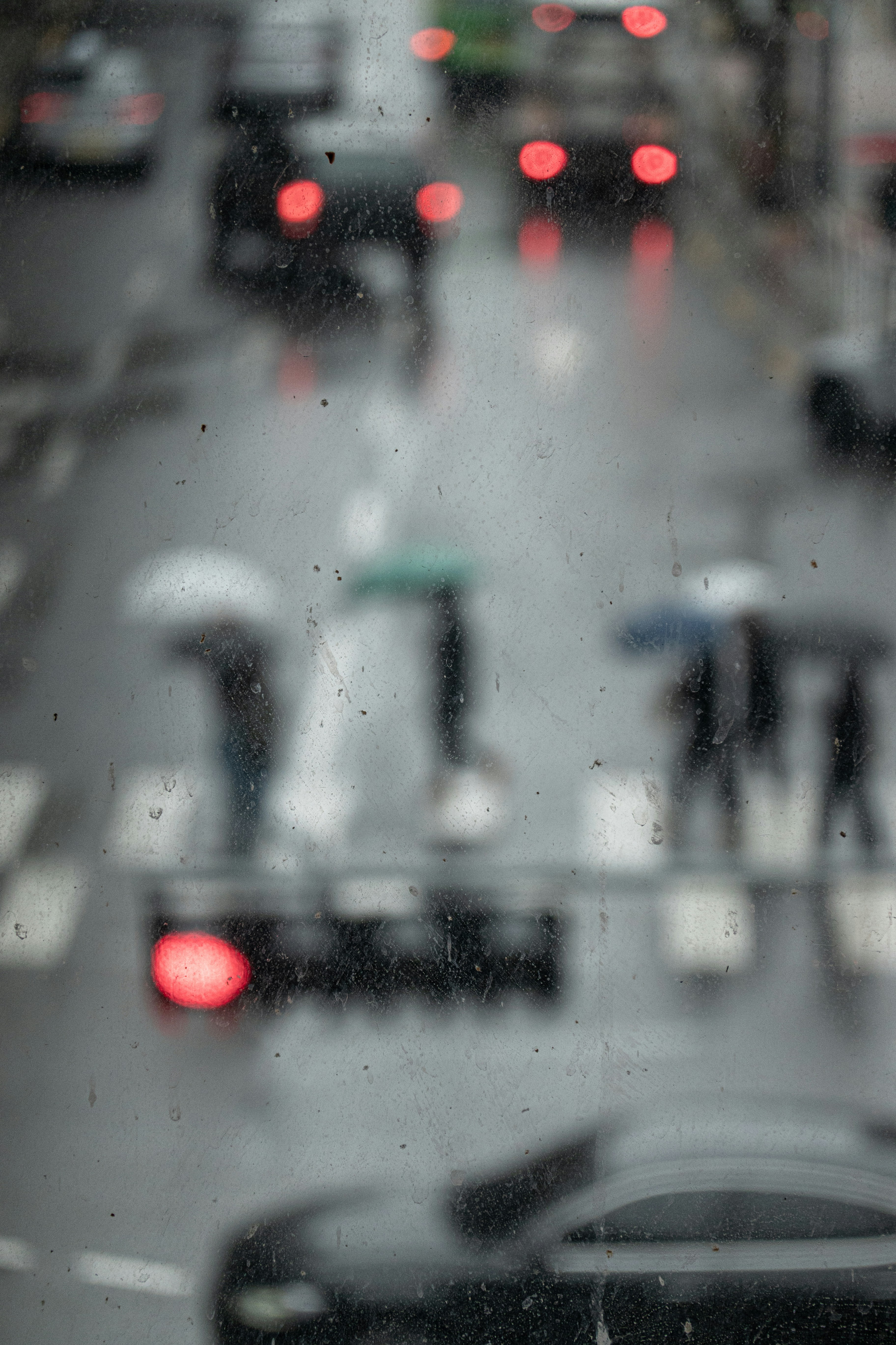 Rain on the Pane: City Shadows and Umbrellas Weaving Past Red Taillights