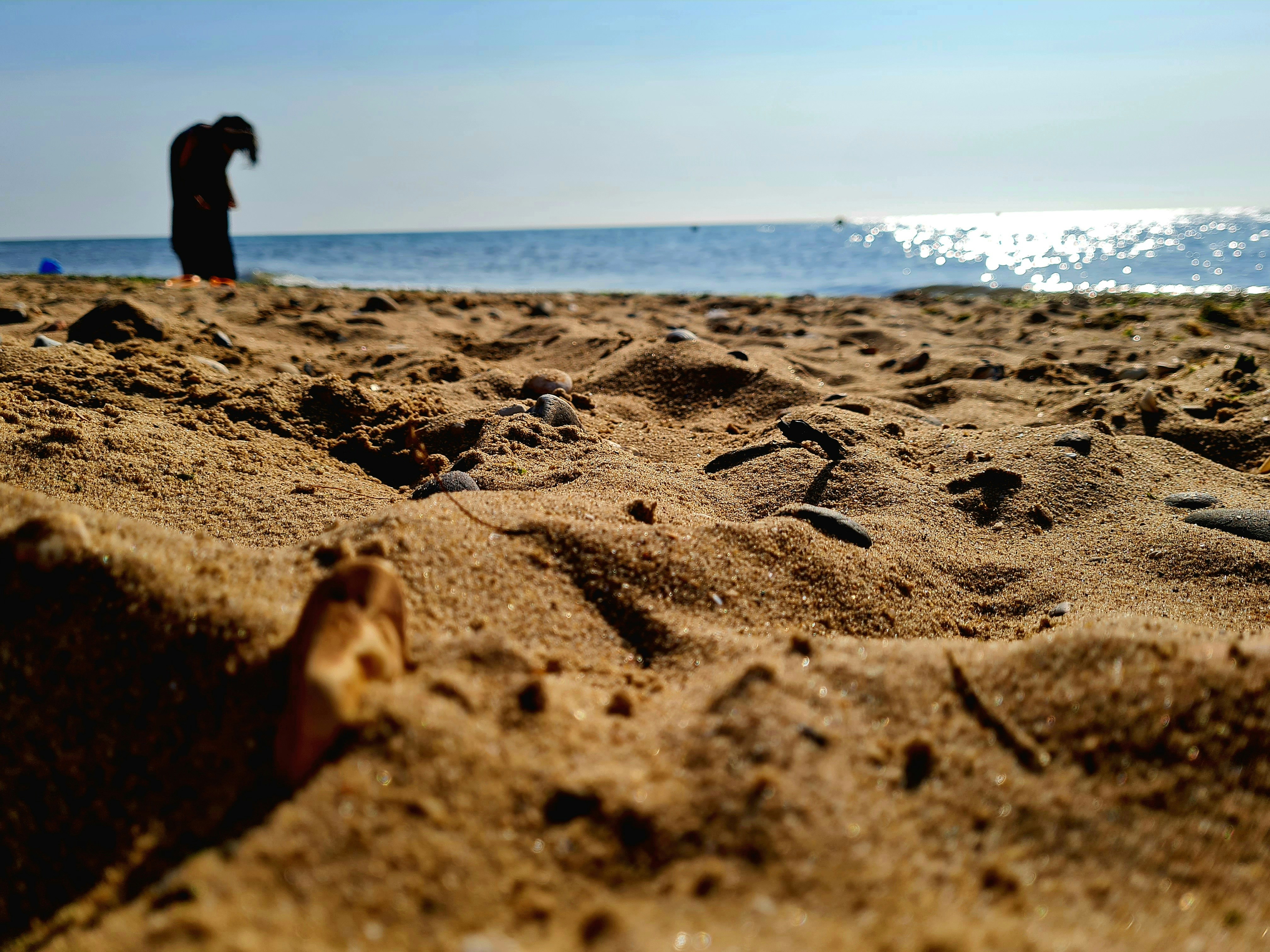 Person standing on a sandy beach with sunlight reflecting off the ocean.