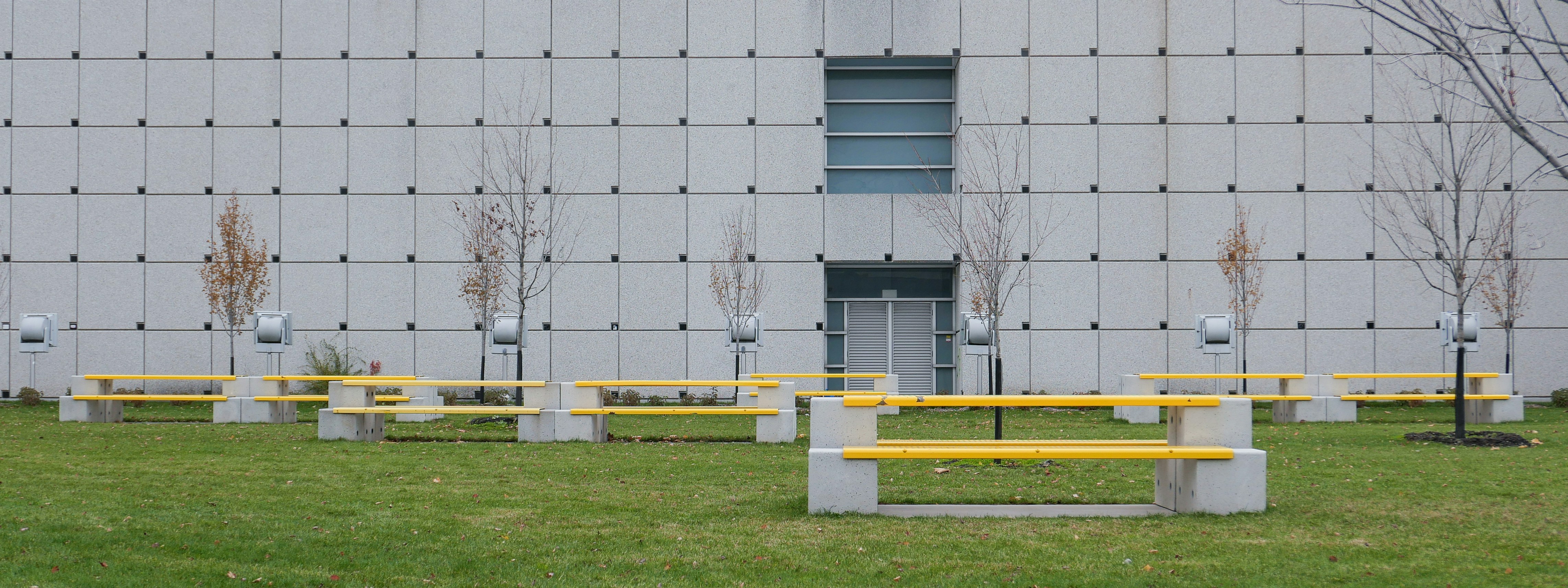 A row of yellow benches sitting in front of a building photo – Free ...