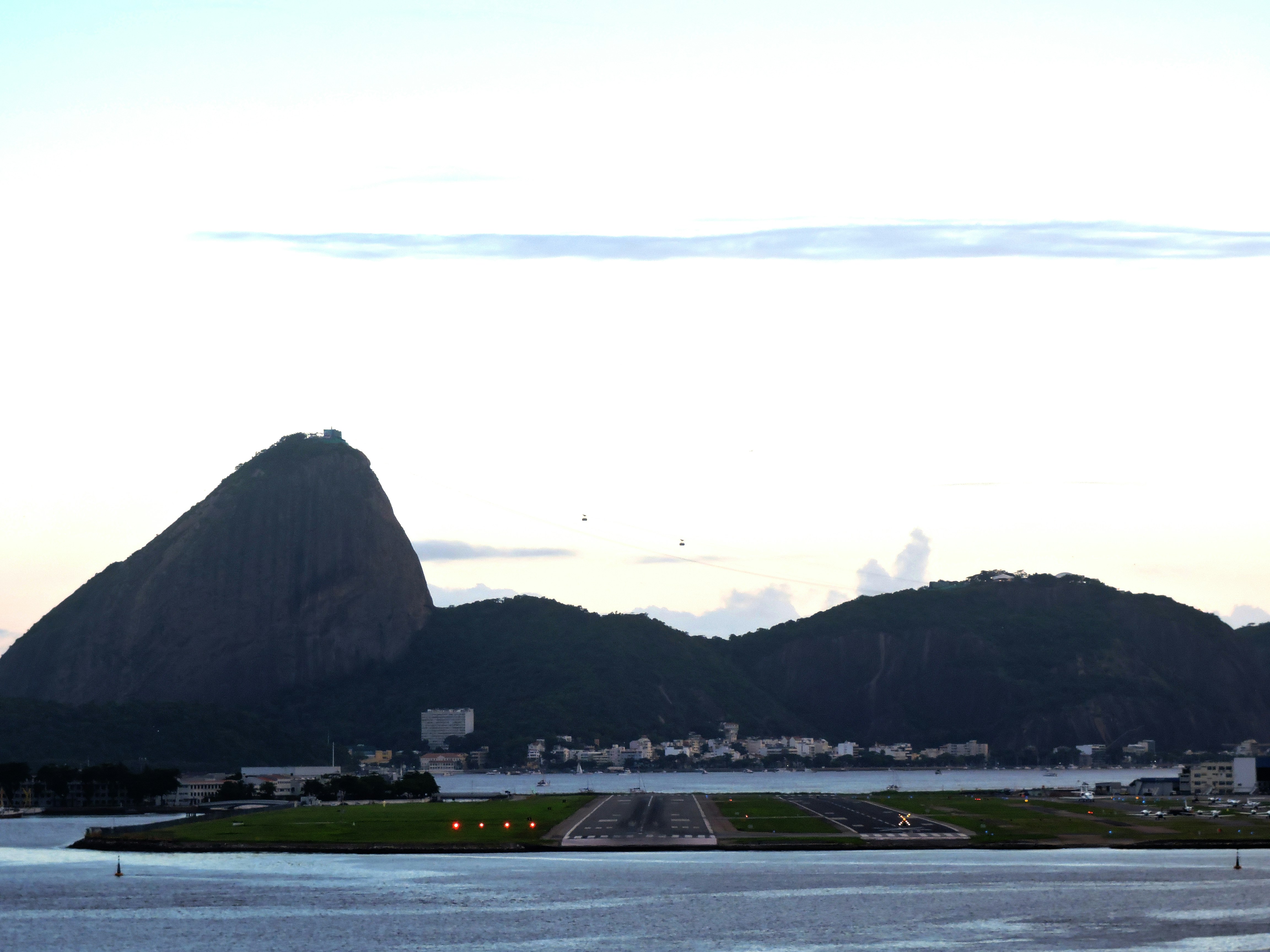 Distant view of an airport runway leading towards the iconic Sugarloaf Mountain at dusk.