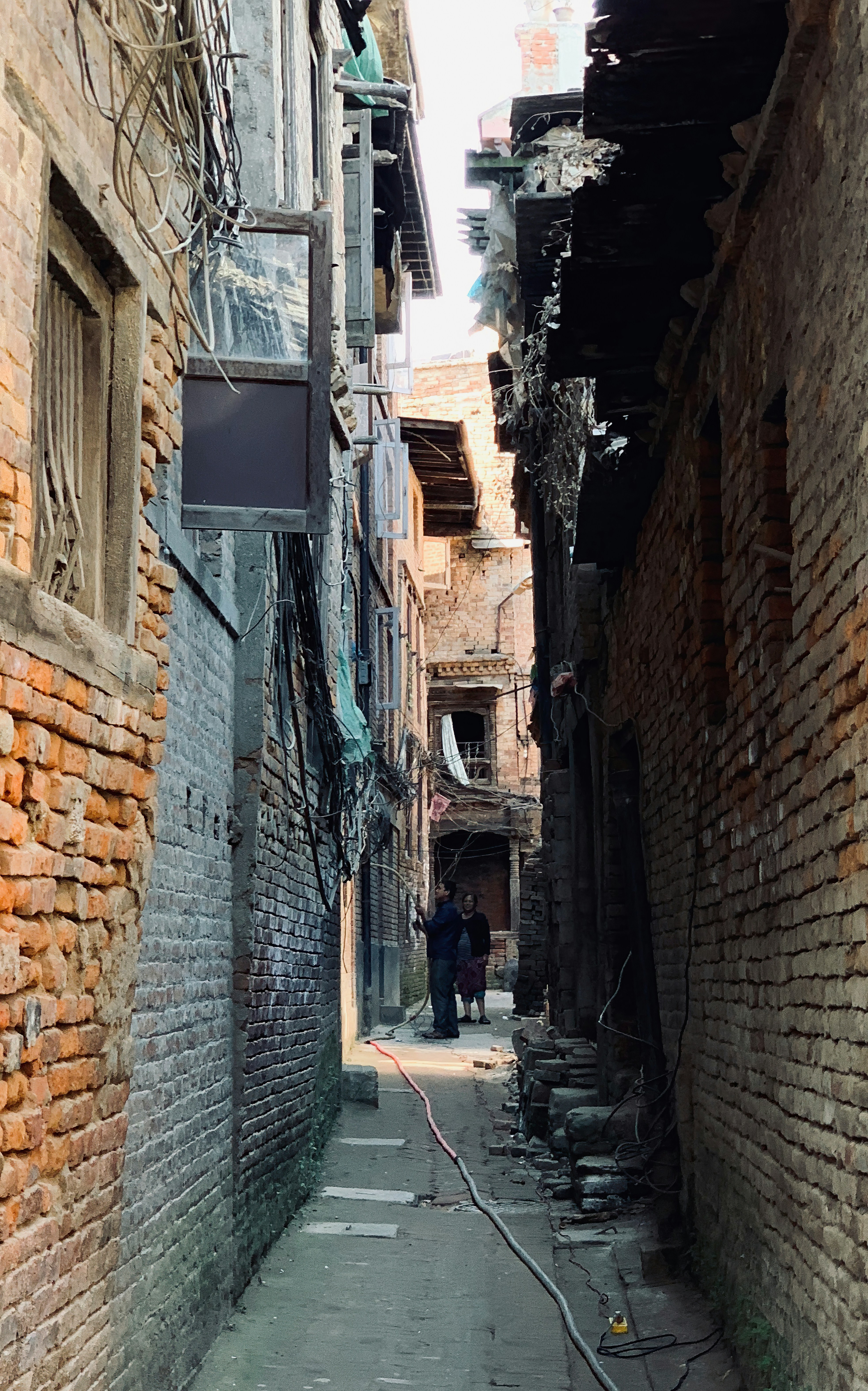 Sunlit Vein: Two Figures at the End of a Narrow Brick Alley