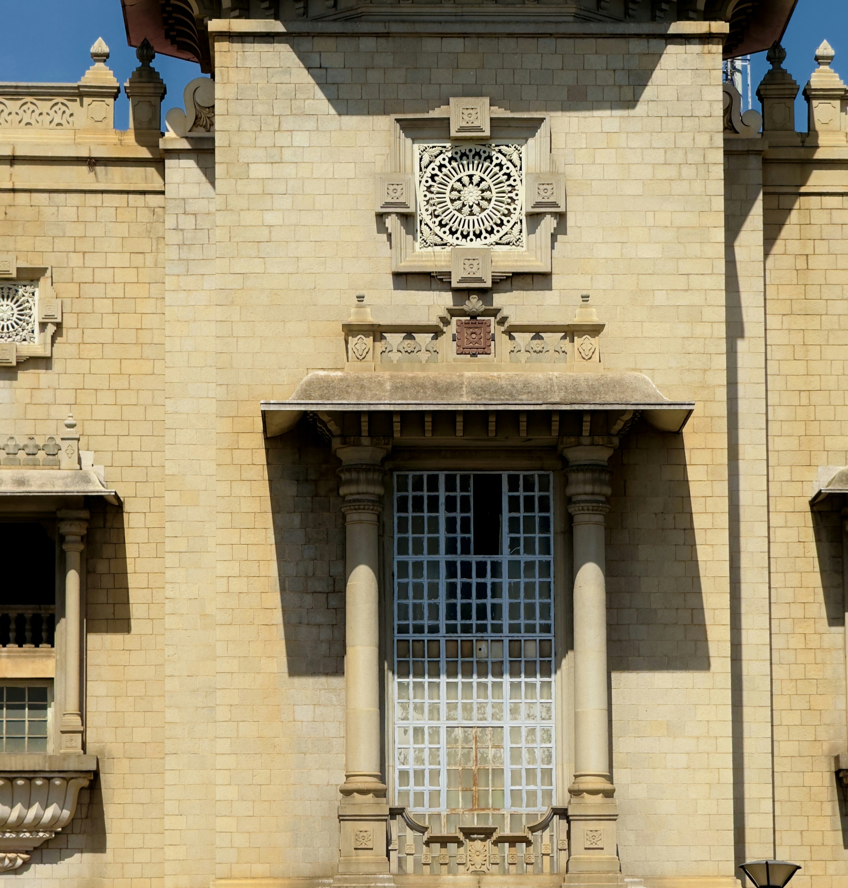 Central Grid Window Framed by Columns on a Sunlit Stone Facade