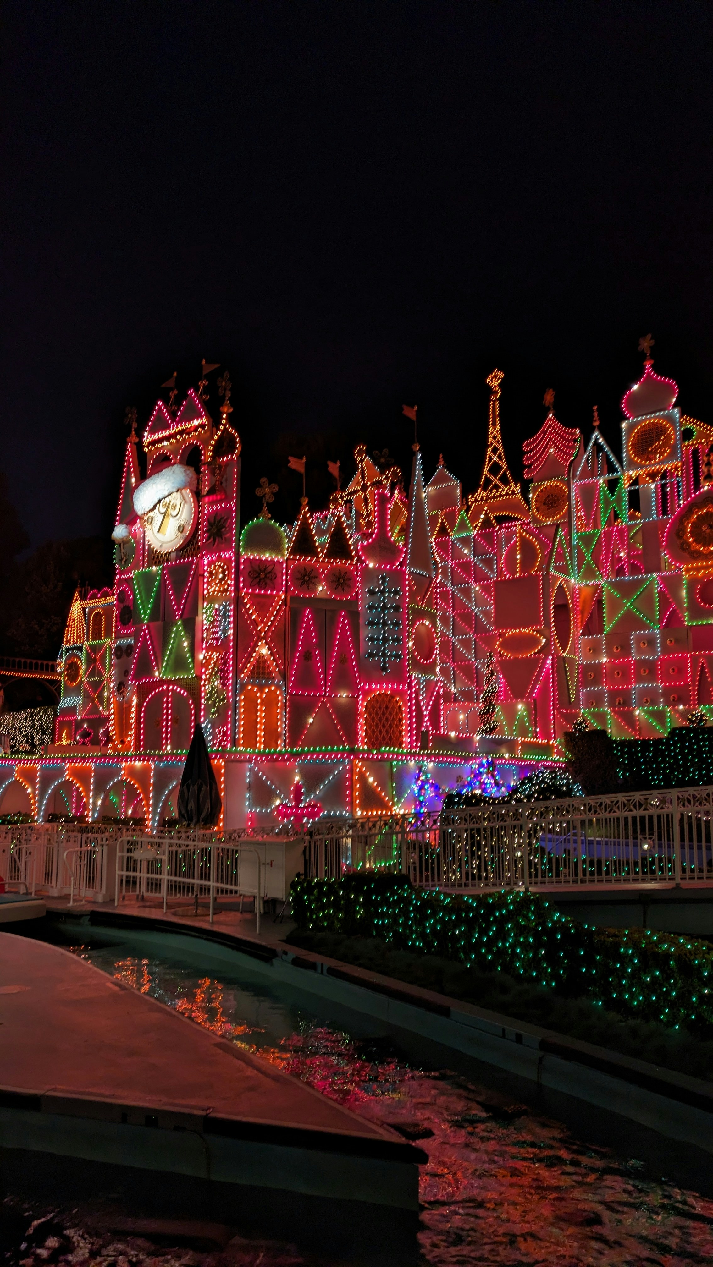 Vibrant illuminated structures adorned with colorful lights at night, creating a whimsical atmosphere. The scene captures the festive spirit of a popular amusement park attraction.