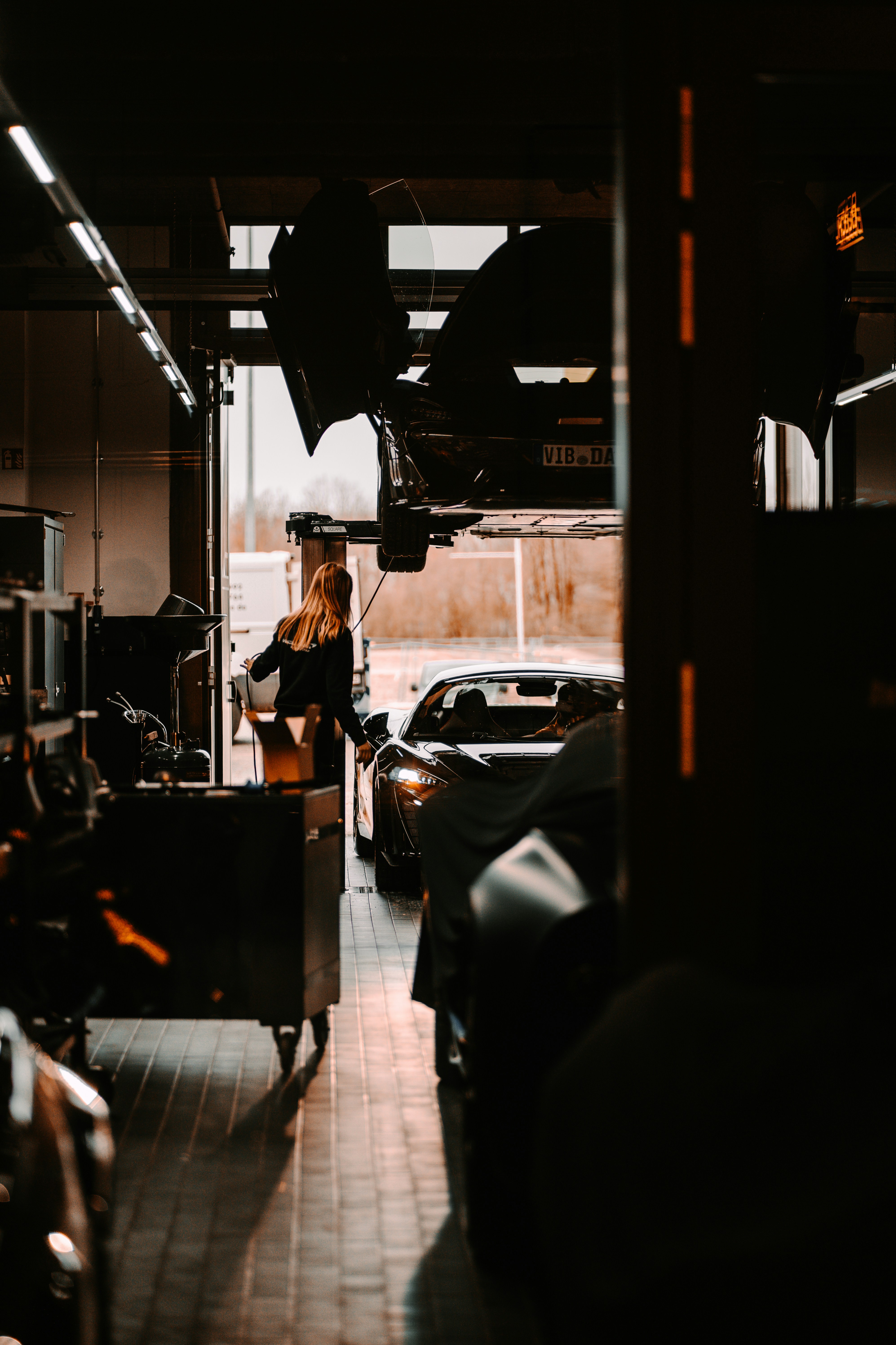 Mid-Shift Gloom: A Woman by a Sleek Car in a Quiet Auto Workshop