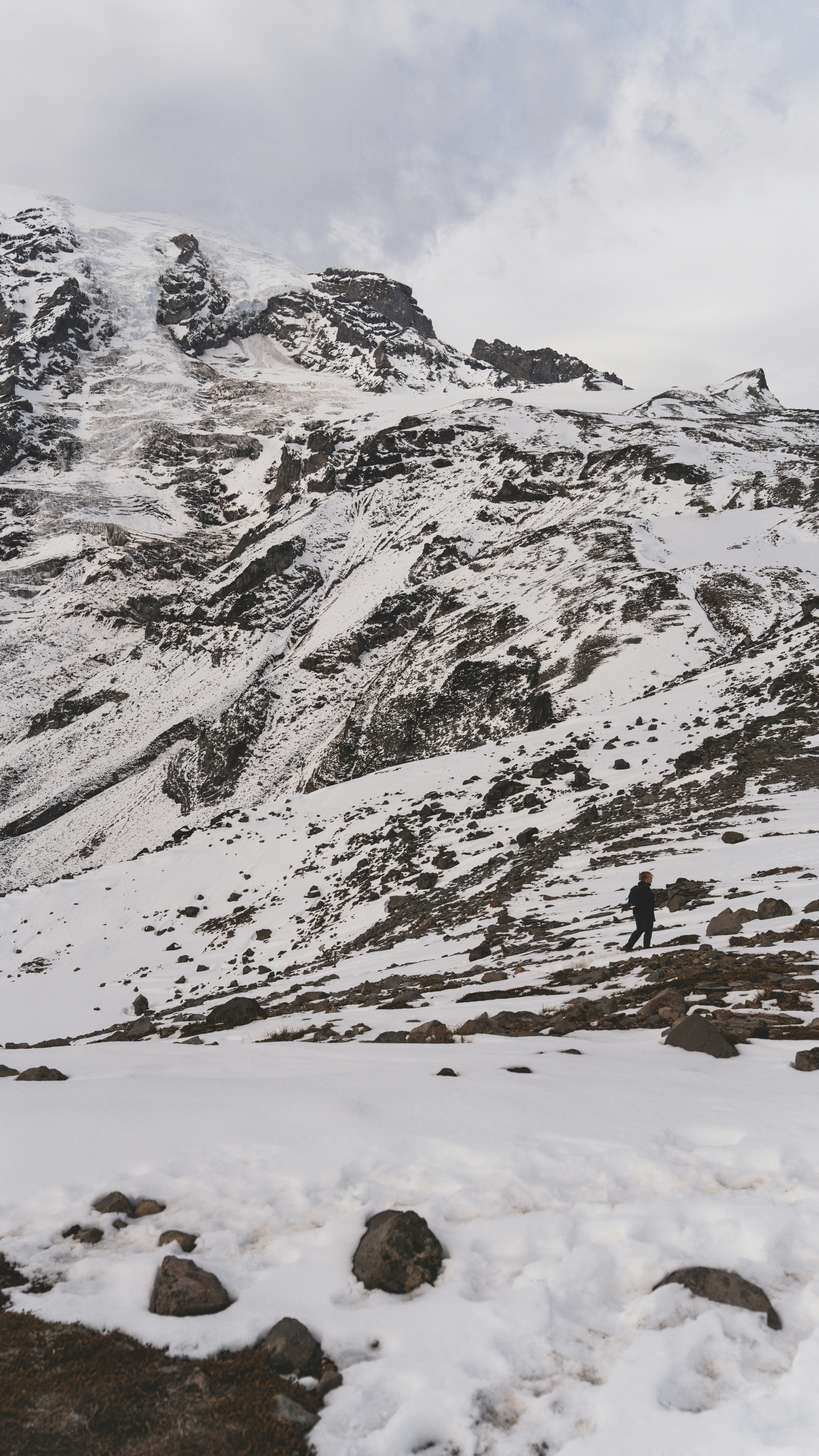 Lone silhouette on a snow-swept ridge beneath jagged alpine peaks