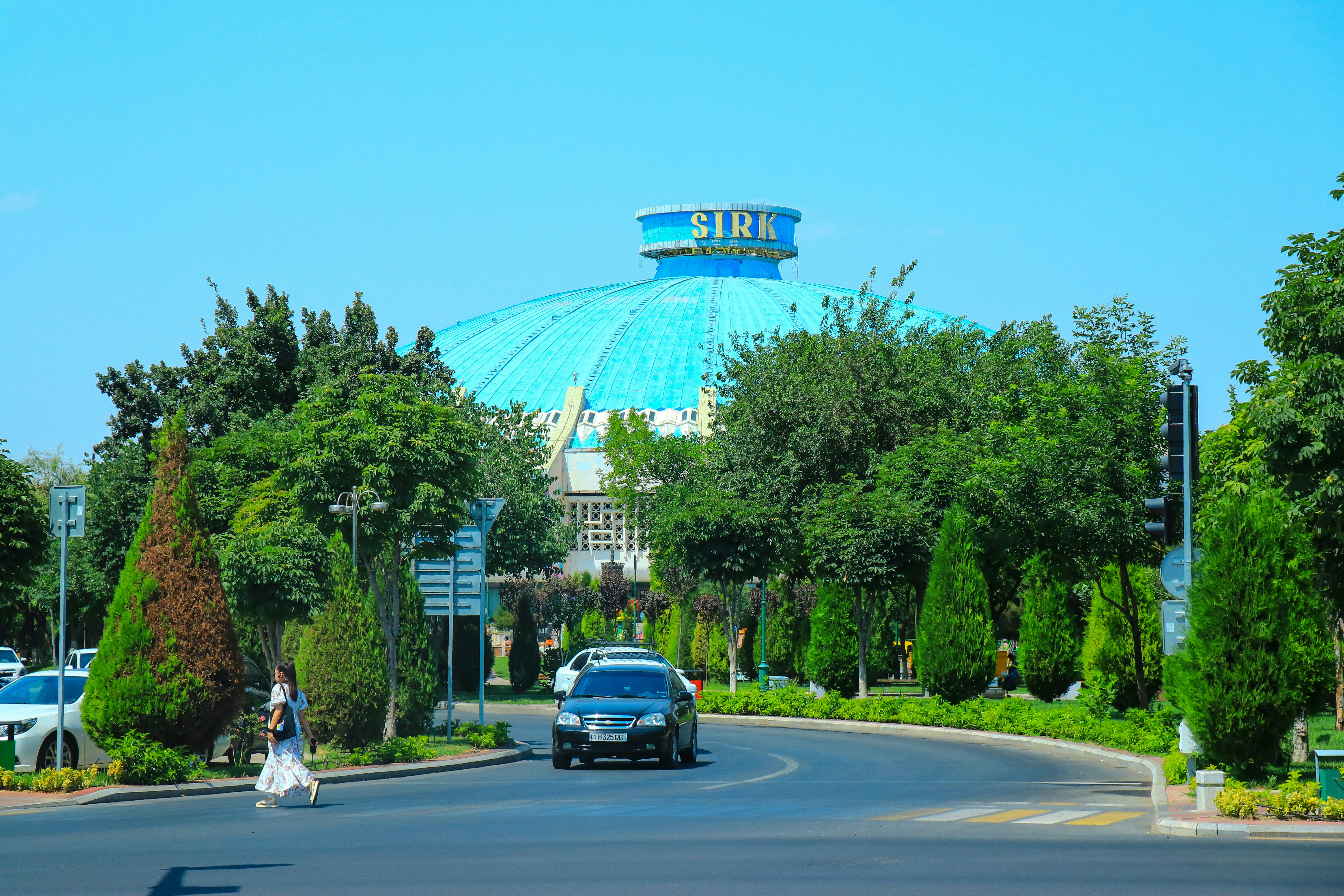 Circular road leading to Tashkent's State Circus, surrounded by lush greenery under a clear blue sky.