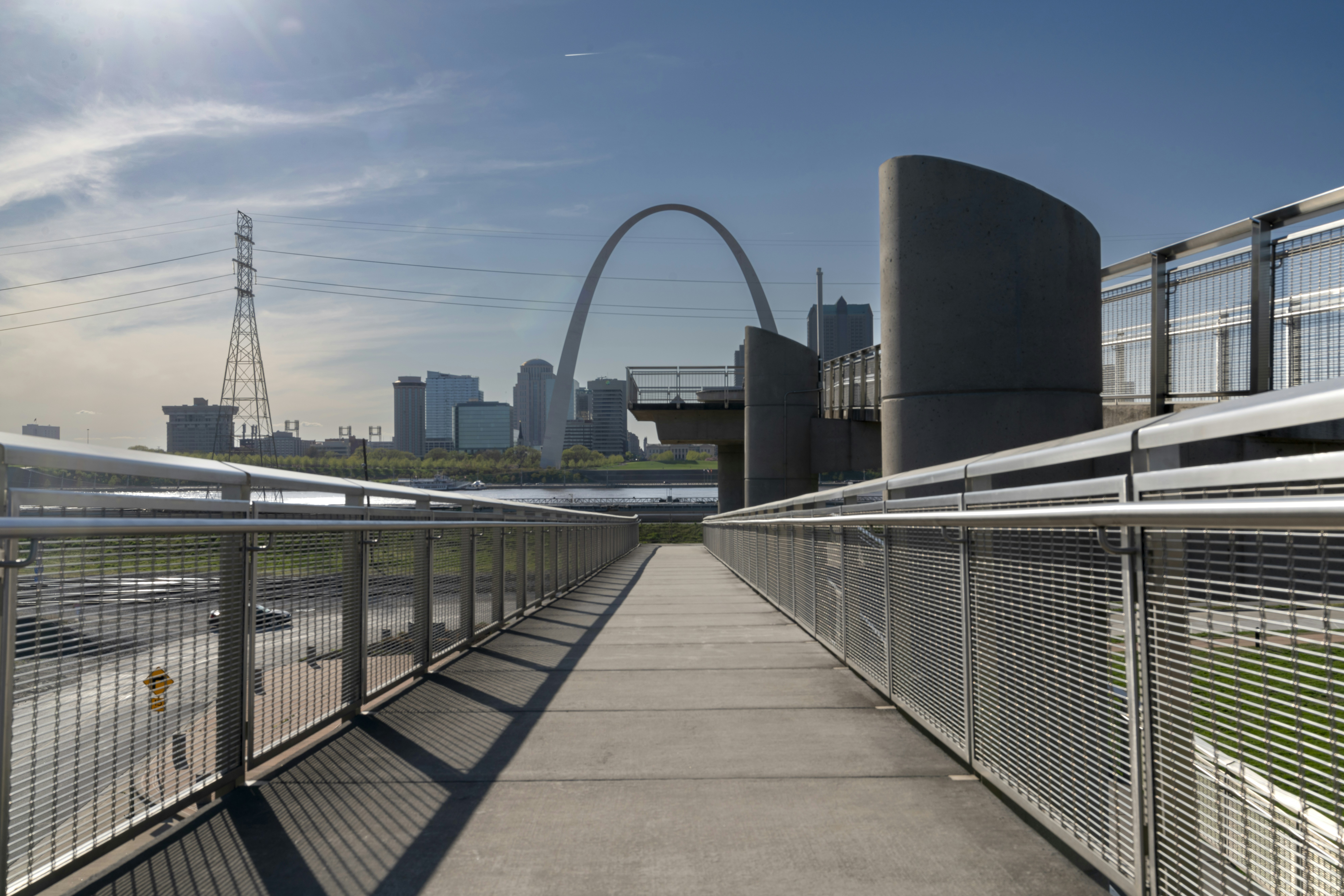 Modern walkway leading toward the Gateway Arch, framed by city skyscrapers under a clear sky.