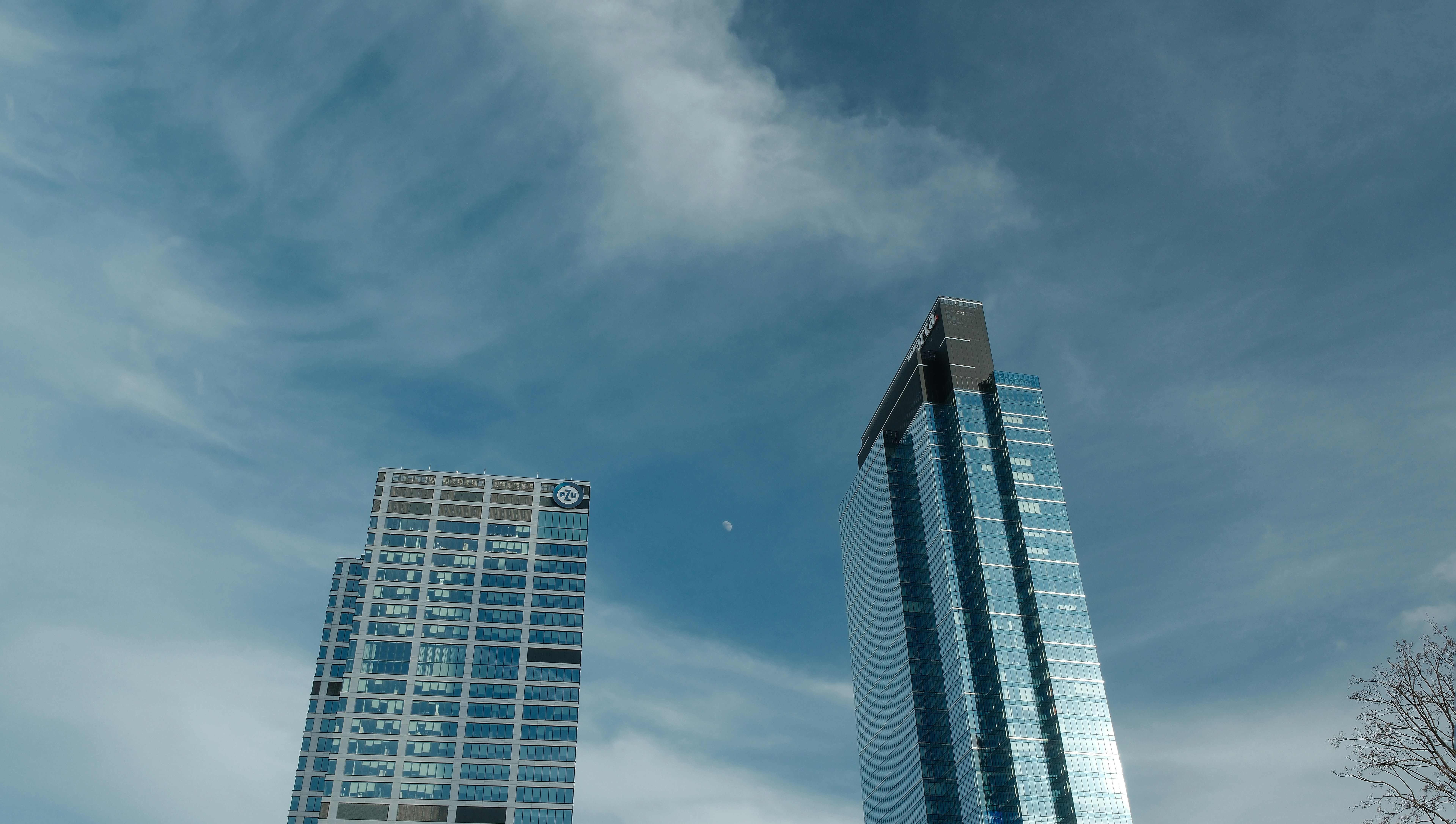 The sight of the beautiful azure sky with two skyscrapers (PZU Tower & "Warta") flanking either side in the center of the Warsaw, Poland. The crescent moon can be observed in the middle, nestled between the two buildings.