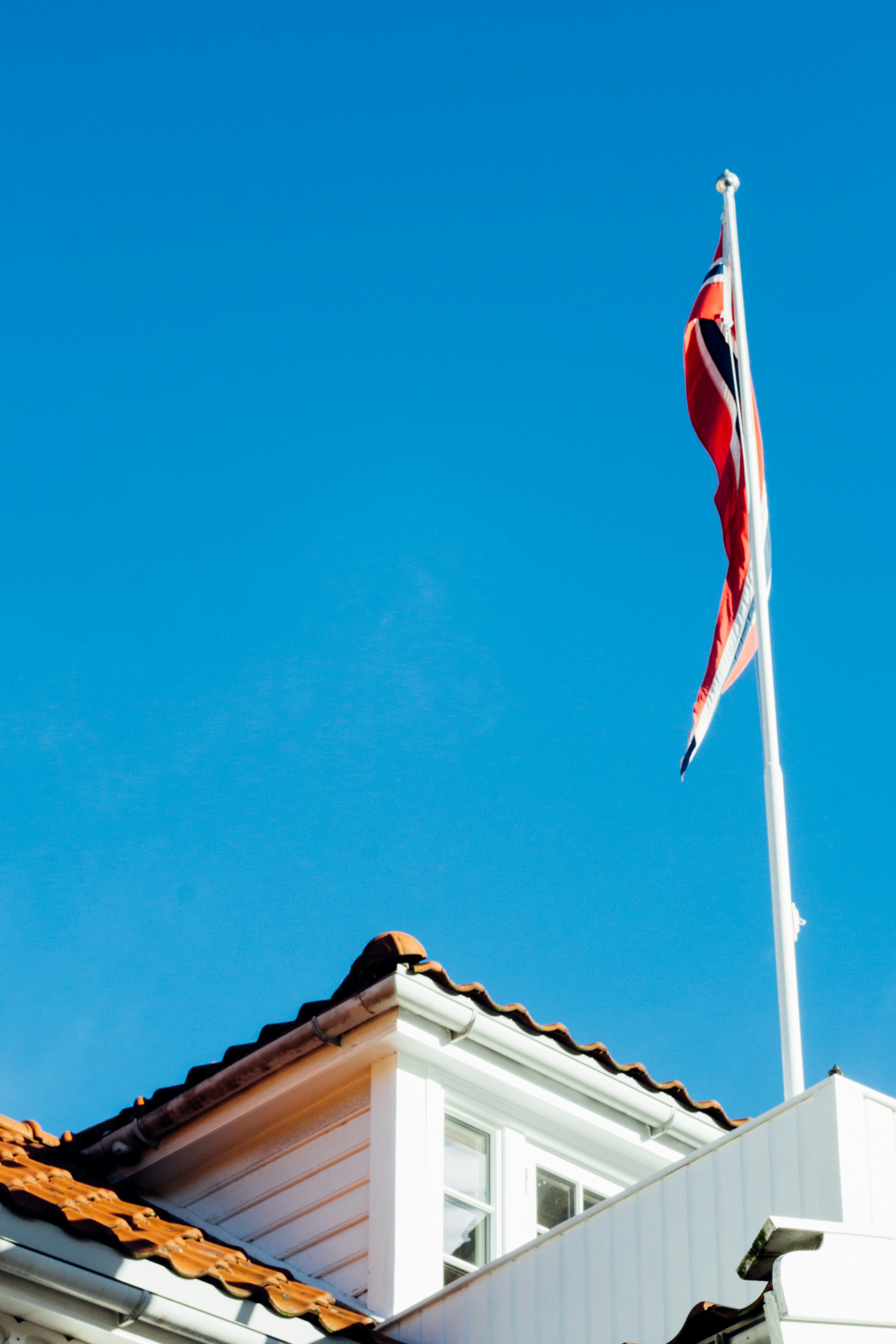 Edge of the Blue: Flagpole Rising Over a White Cottage Under a Pristine Sky