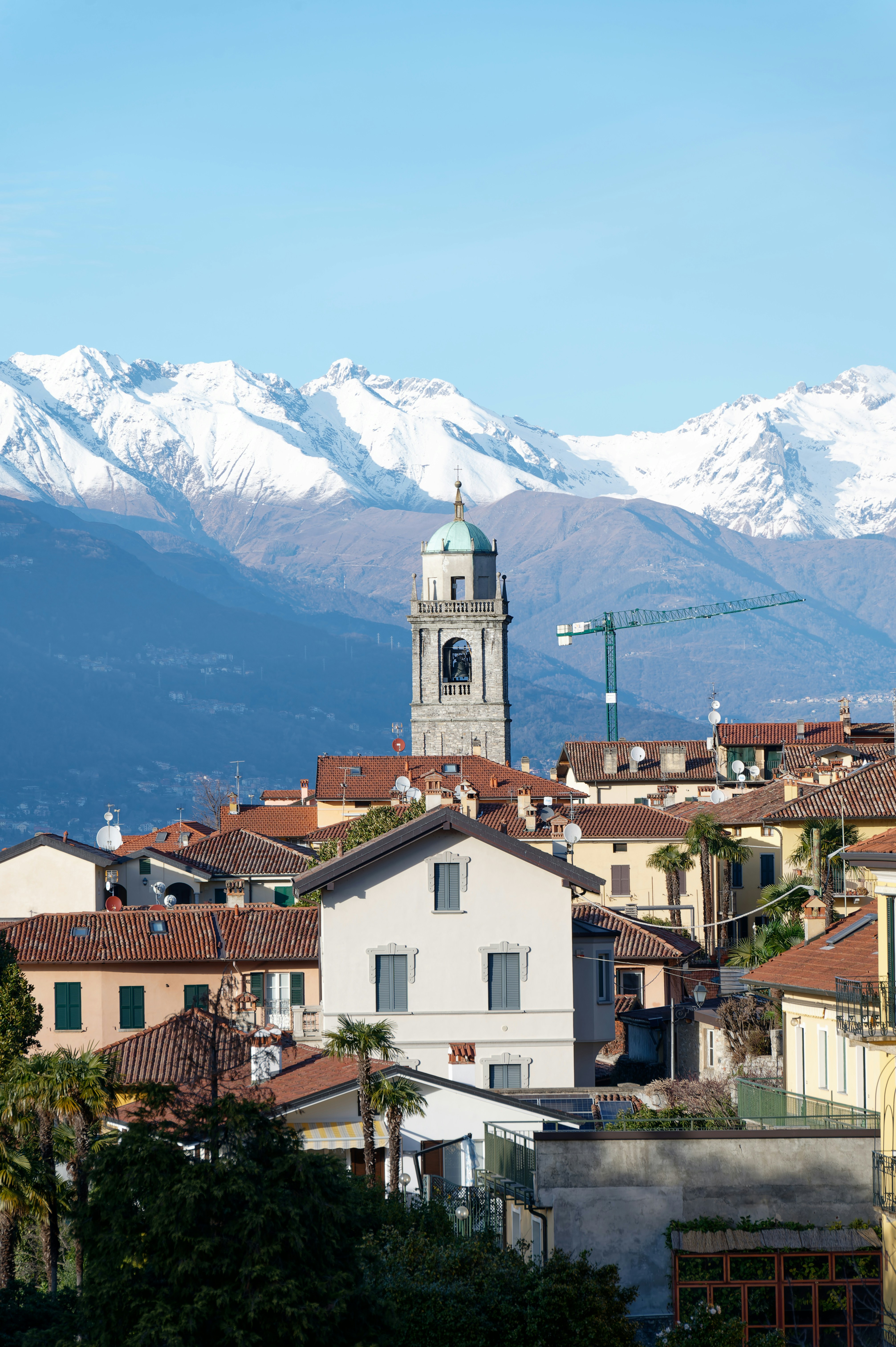 Bell Tower Over Red-Tiled Village Beneath Snow-Capped Alps