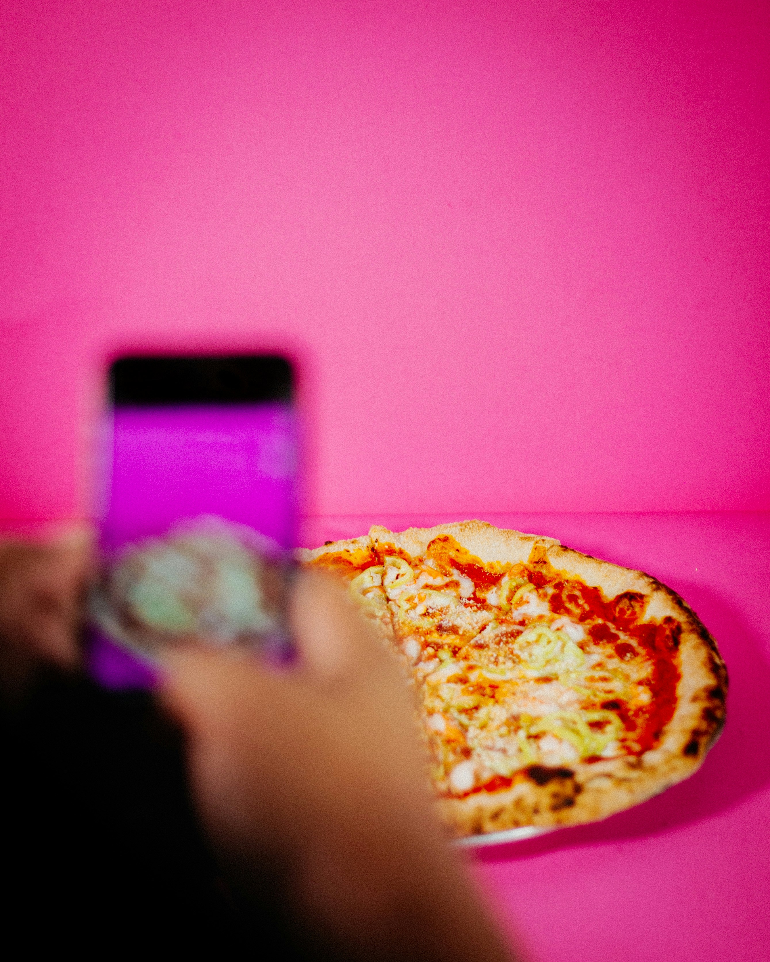 Pizza in the Frame: A Blurred Phone Front and a Slice on Pink