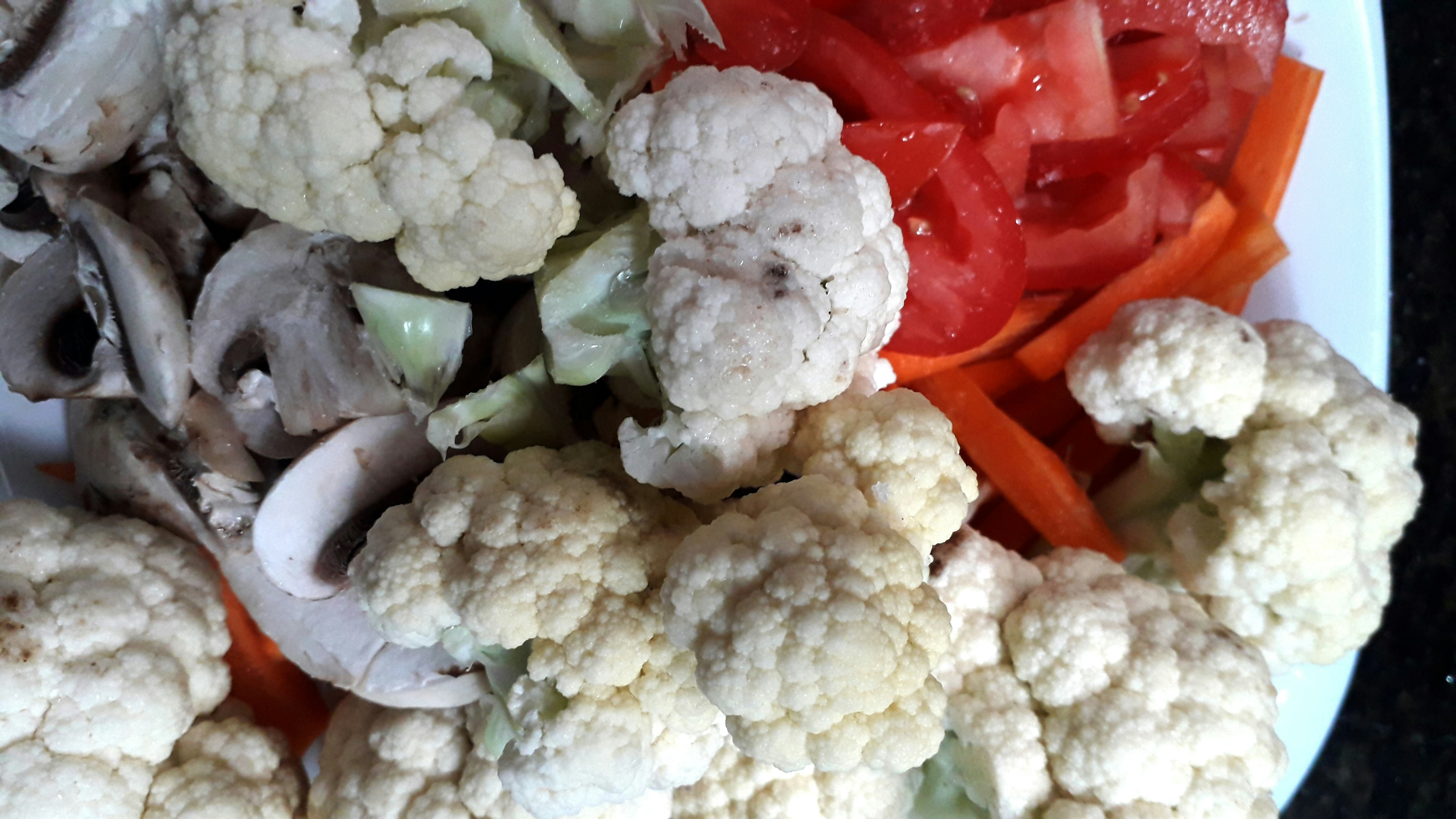 A close-up of chopped vegetables on a plate, featuring cauliflower florets, red peppers, carrots, and mushrooms.