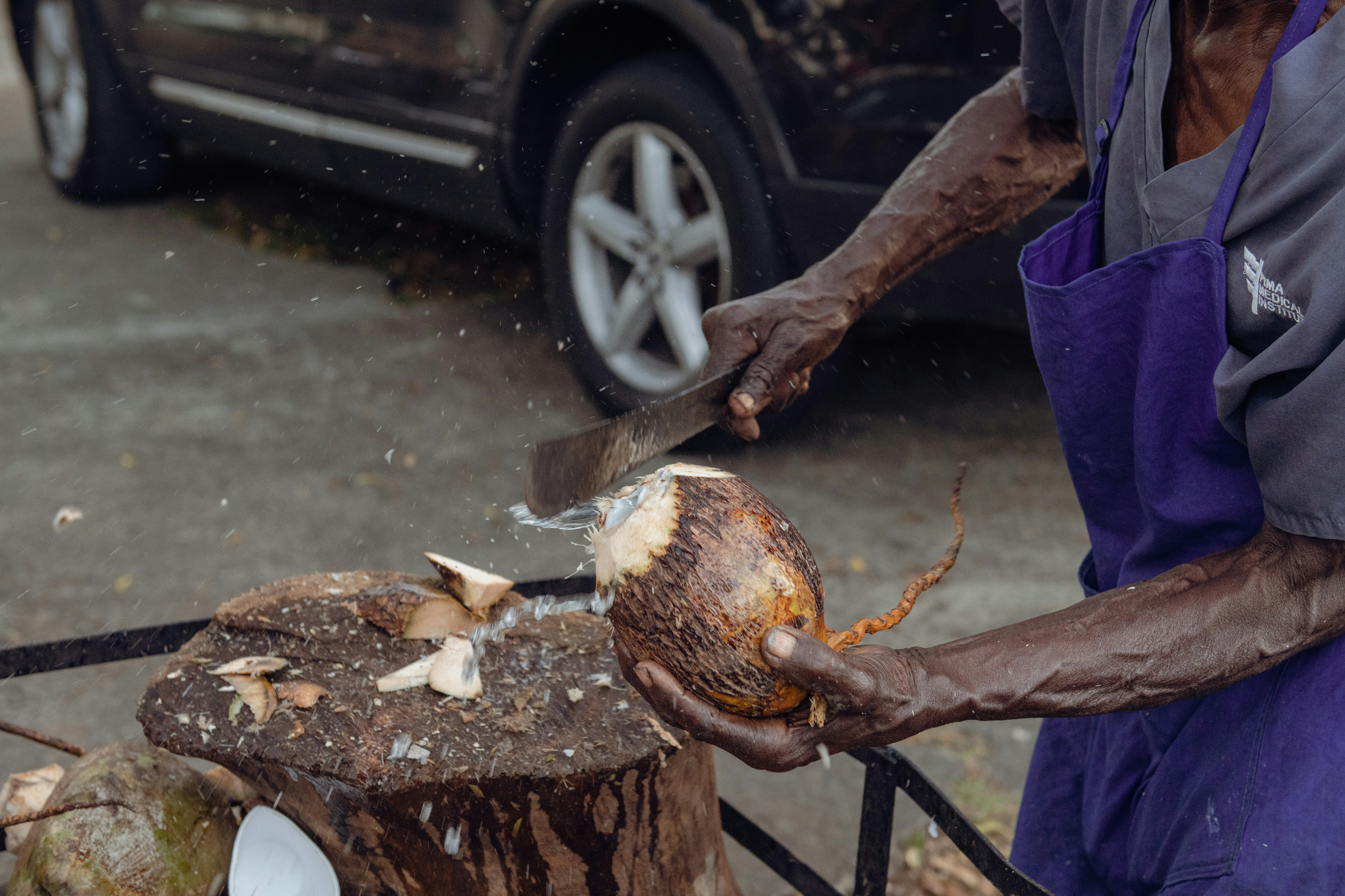 Person skillfully cutting a coconut with a large knife on a wooden stump.