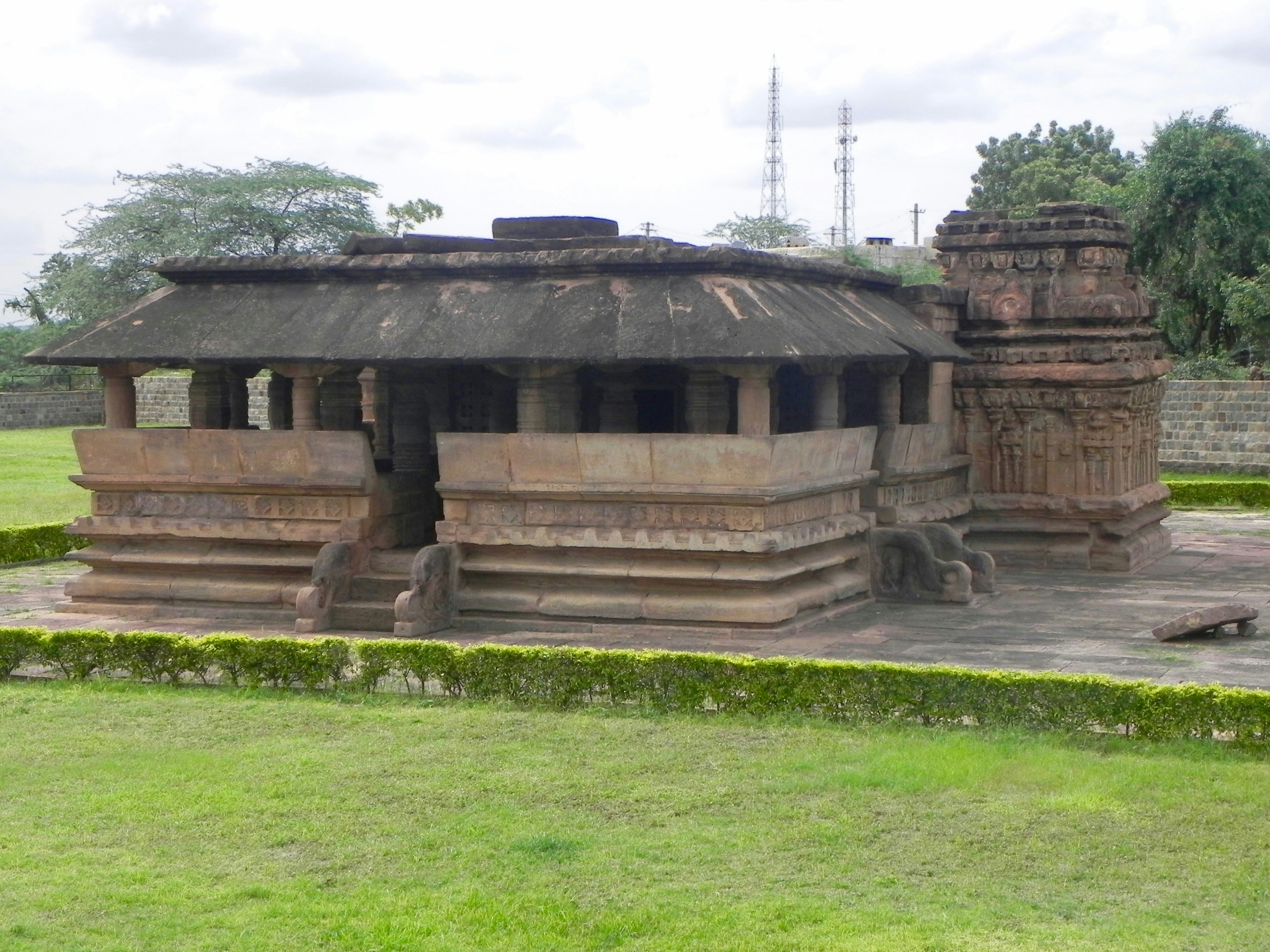 Weathered stone temple ruin on a grassy field with a low wall in the background, captured as a tranquil historical photograph.