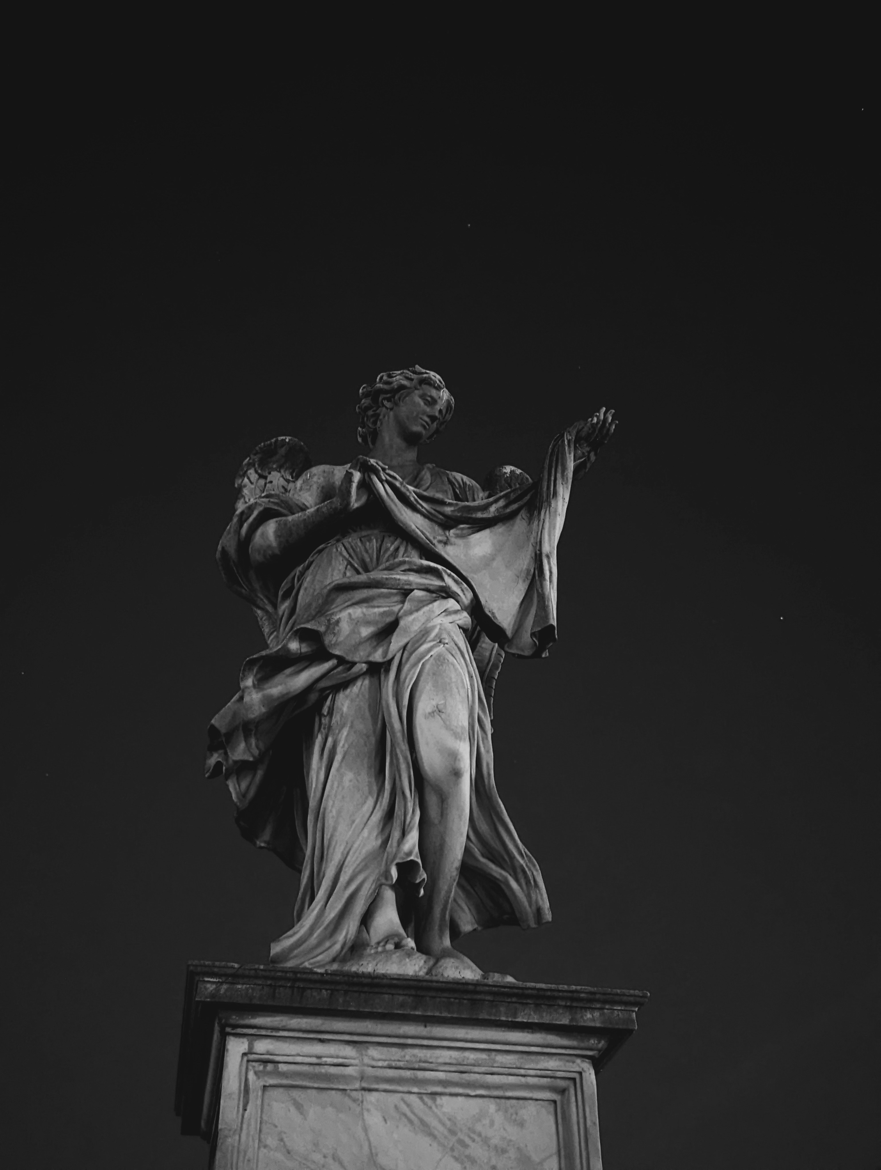A marble statue of a figure draped in flowing garments, cradling a child, set against a dark sky. The artistry captures a moment of tenderness and grace.