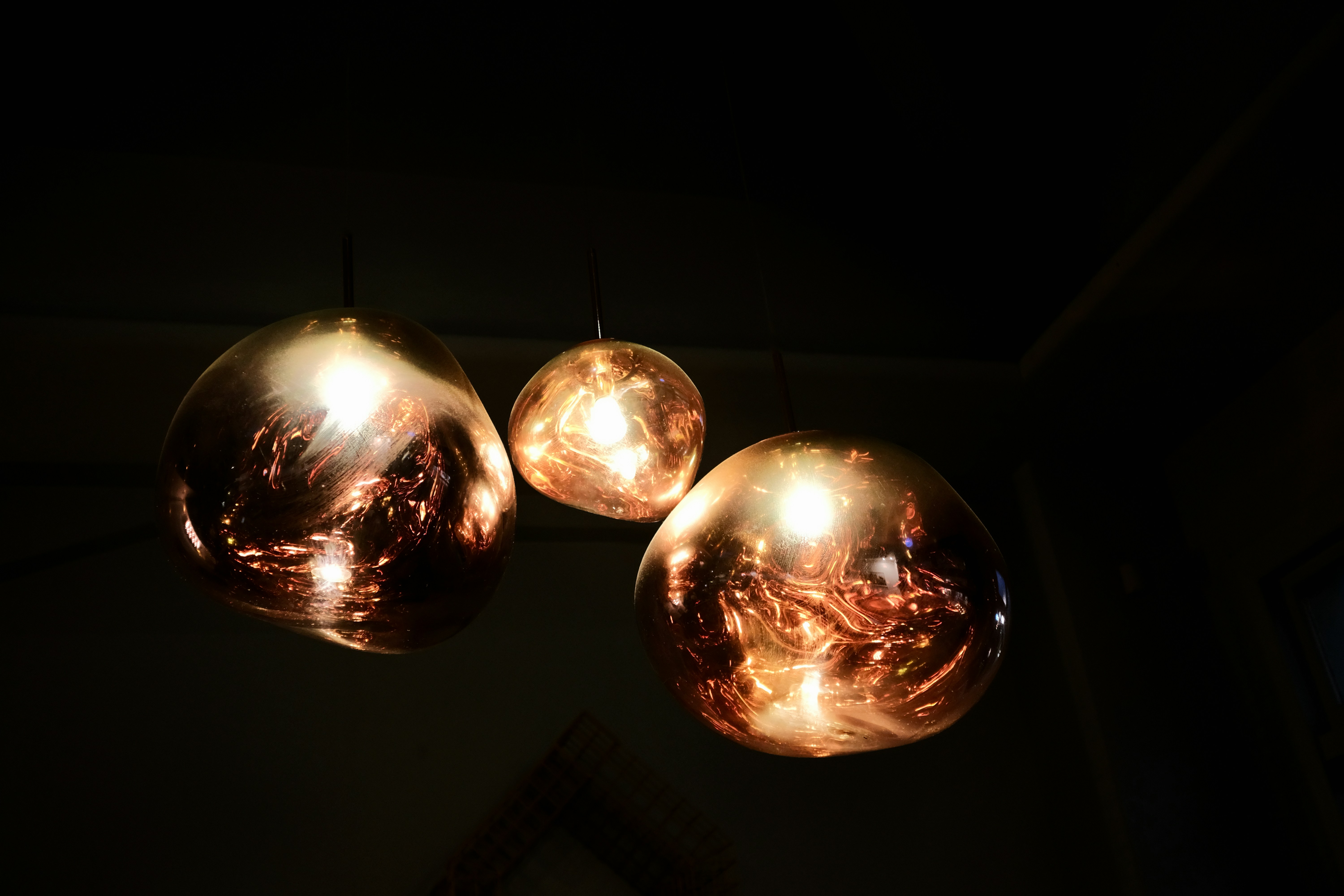 Three glowing spherical lights suspended against a dark ceiling, casting warm reflections.