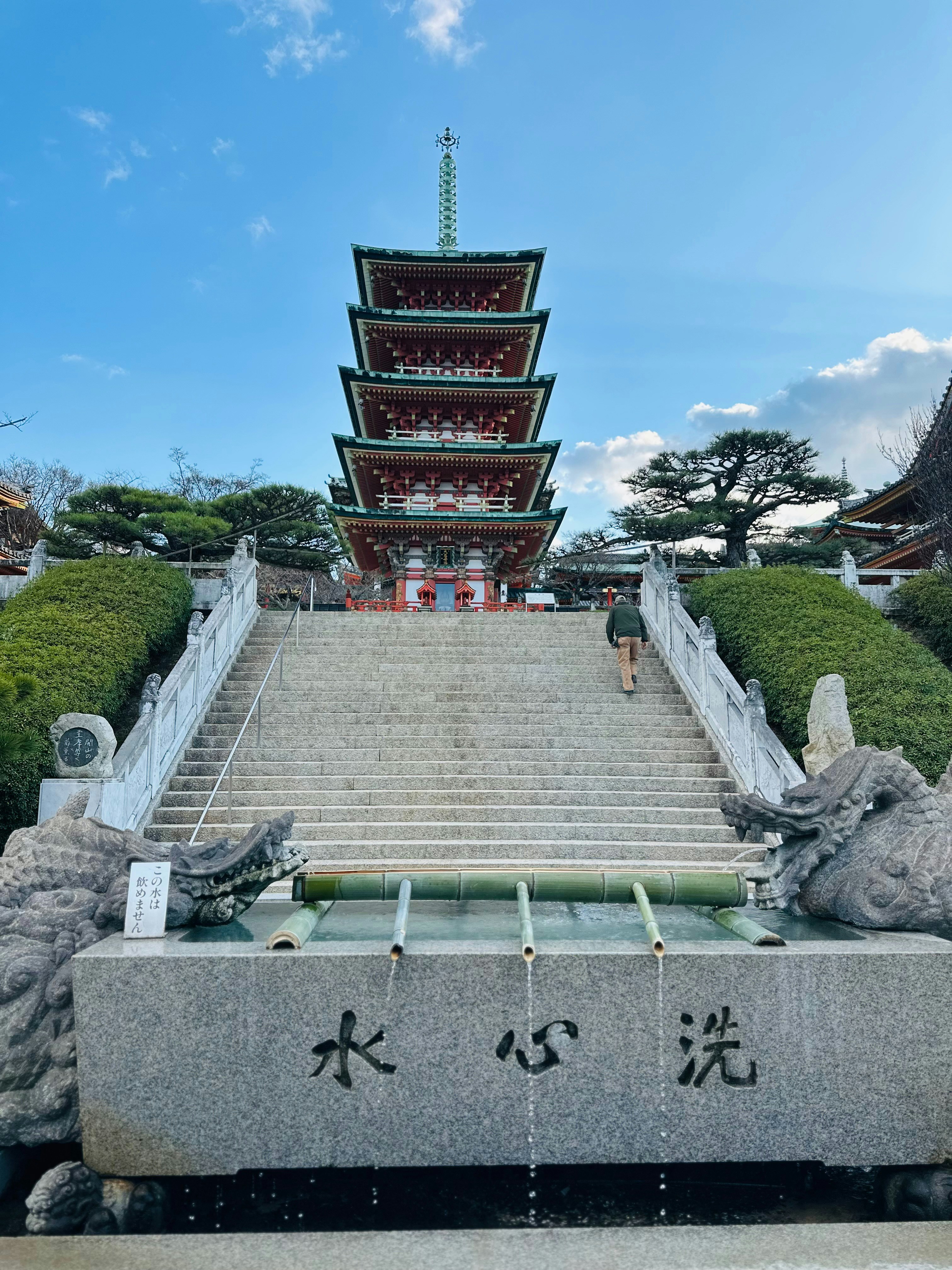 A majestic pagoda rises above stone steps adorned with dragon sculptures, inviting visitors to a tranquil destination. Lush greenery frames the path, enhancing the serene atmosphere.