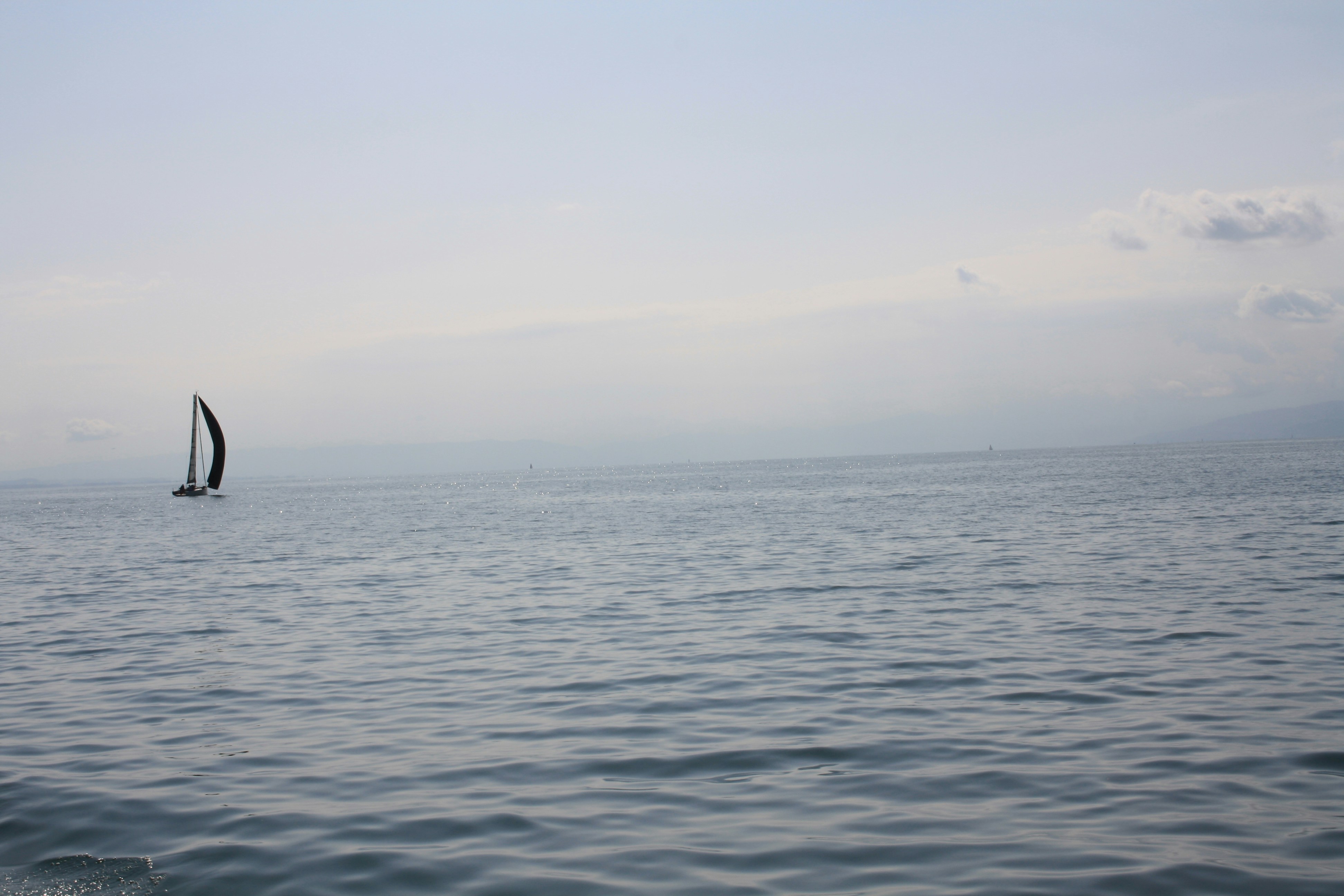 Leftmost Sailboat on a Glassy Sea Under a Pale Sky