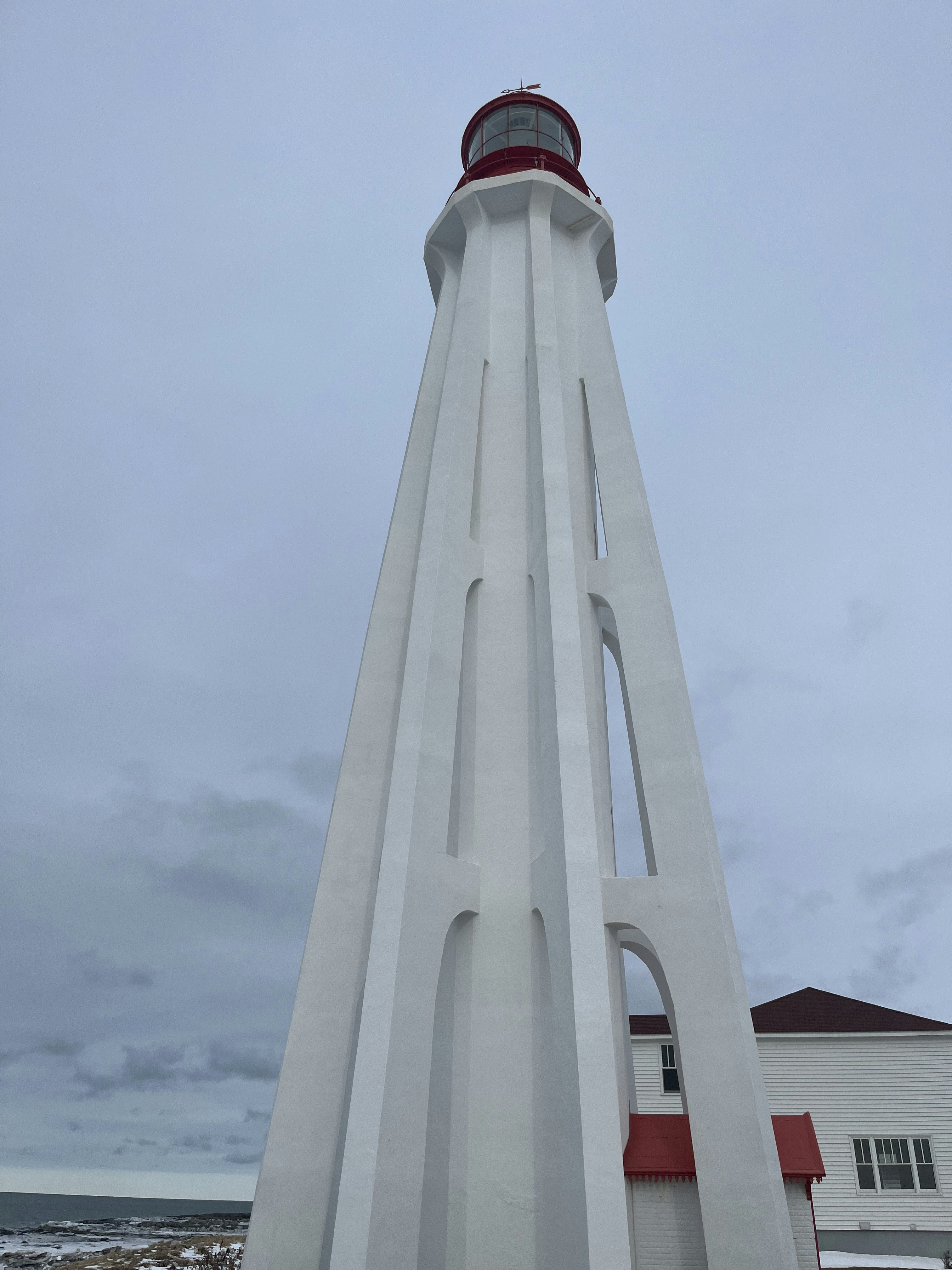 Vertical Beacon: White Lighthouse Rising Over a Red-Roofed Coastline Under Nimbus Clouds