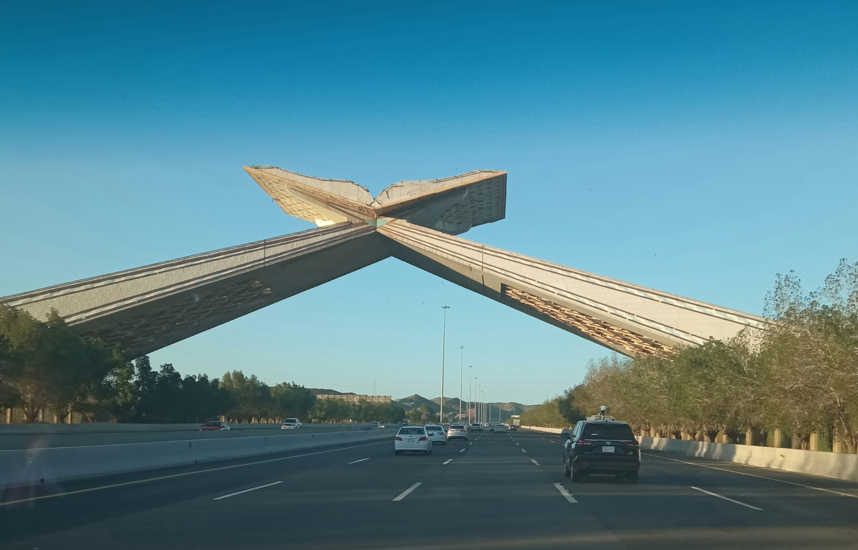 Symmetrical concrete arches span across a busy highway under a clear blue sky.