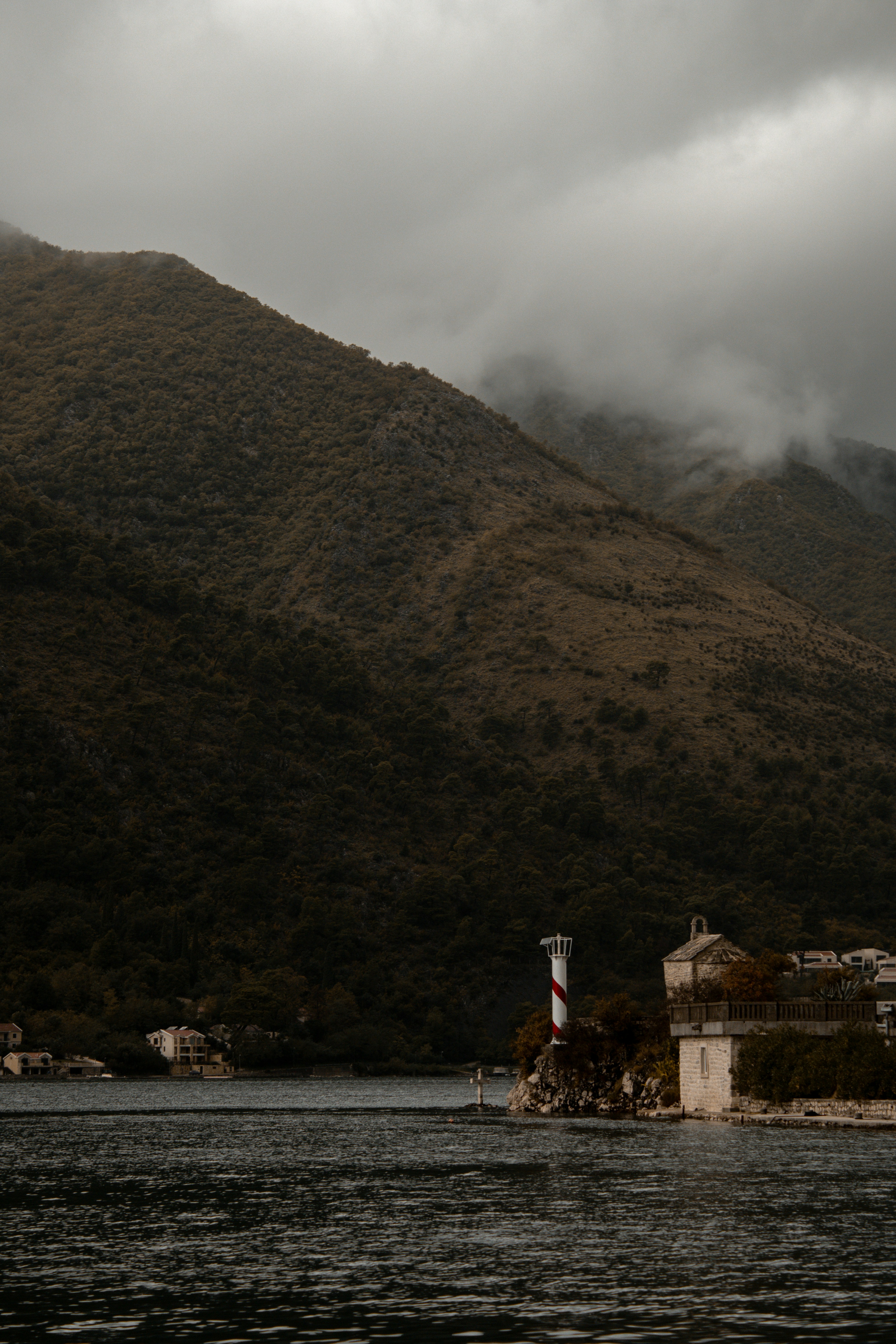 Beacon by Mist: A Lighthouse Guarding a Quiet Harbor Beneath Fog-Wrapped Peaks