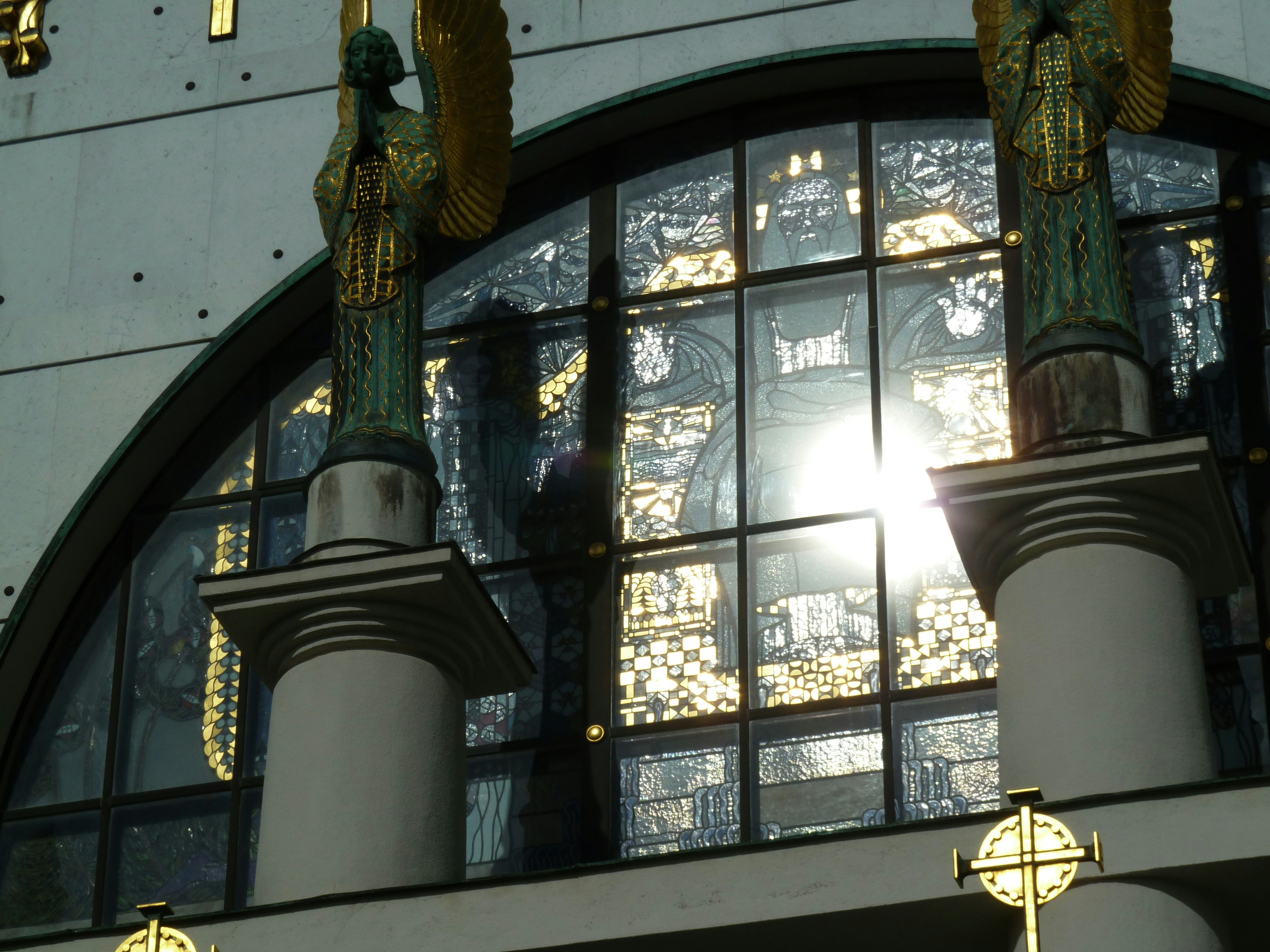 Art Nouveau sculptures and stained glass window illuminated by sunlight on a historic church facade.