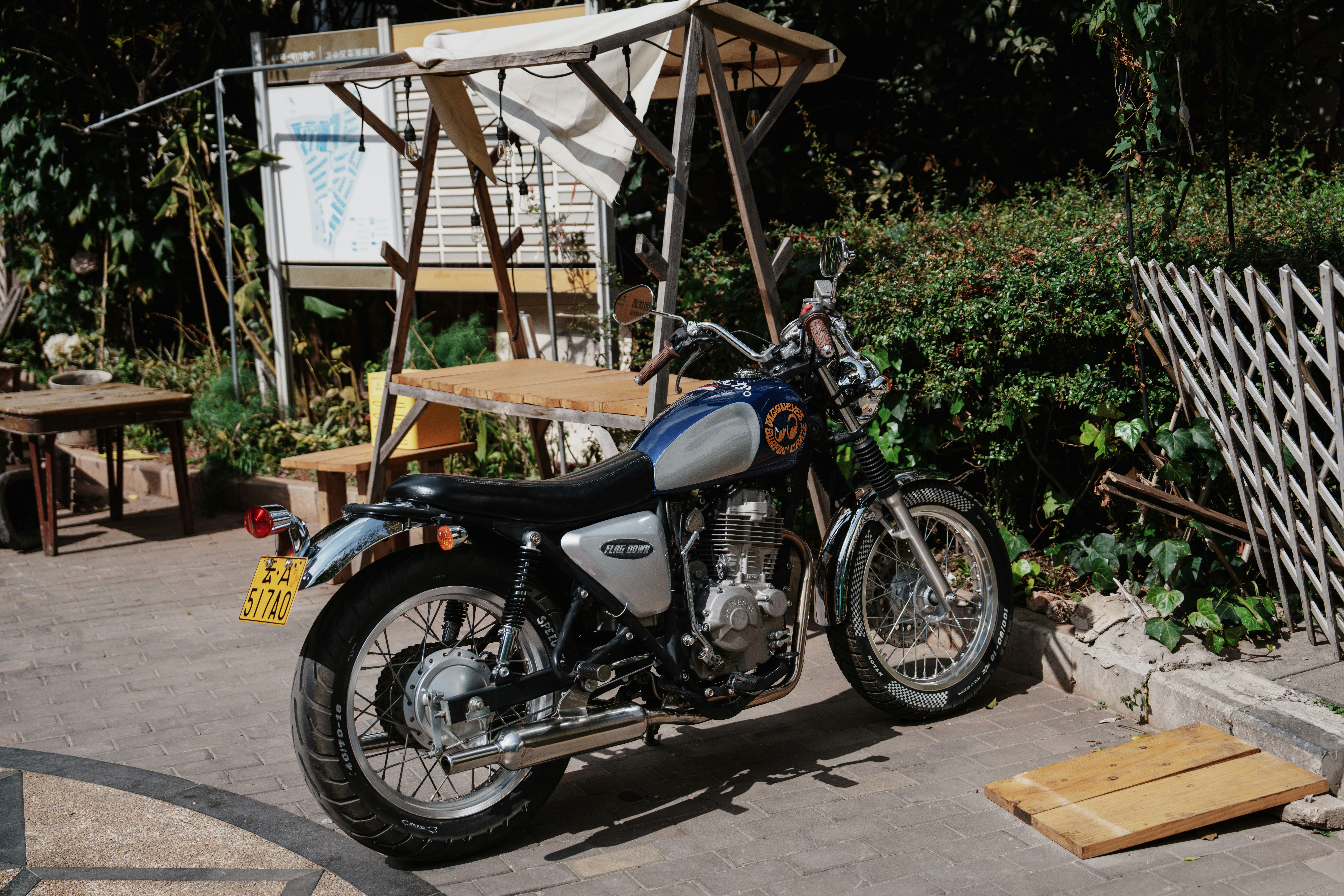 Classic motorcycle resting in a sunlit garden patio beside a rustic wooden bench.