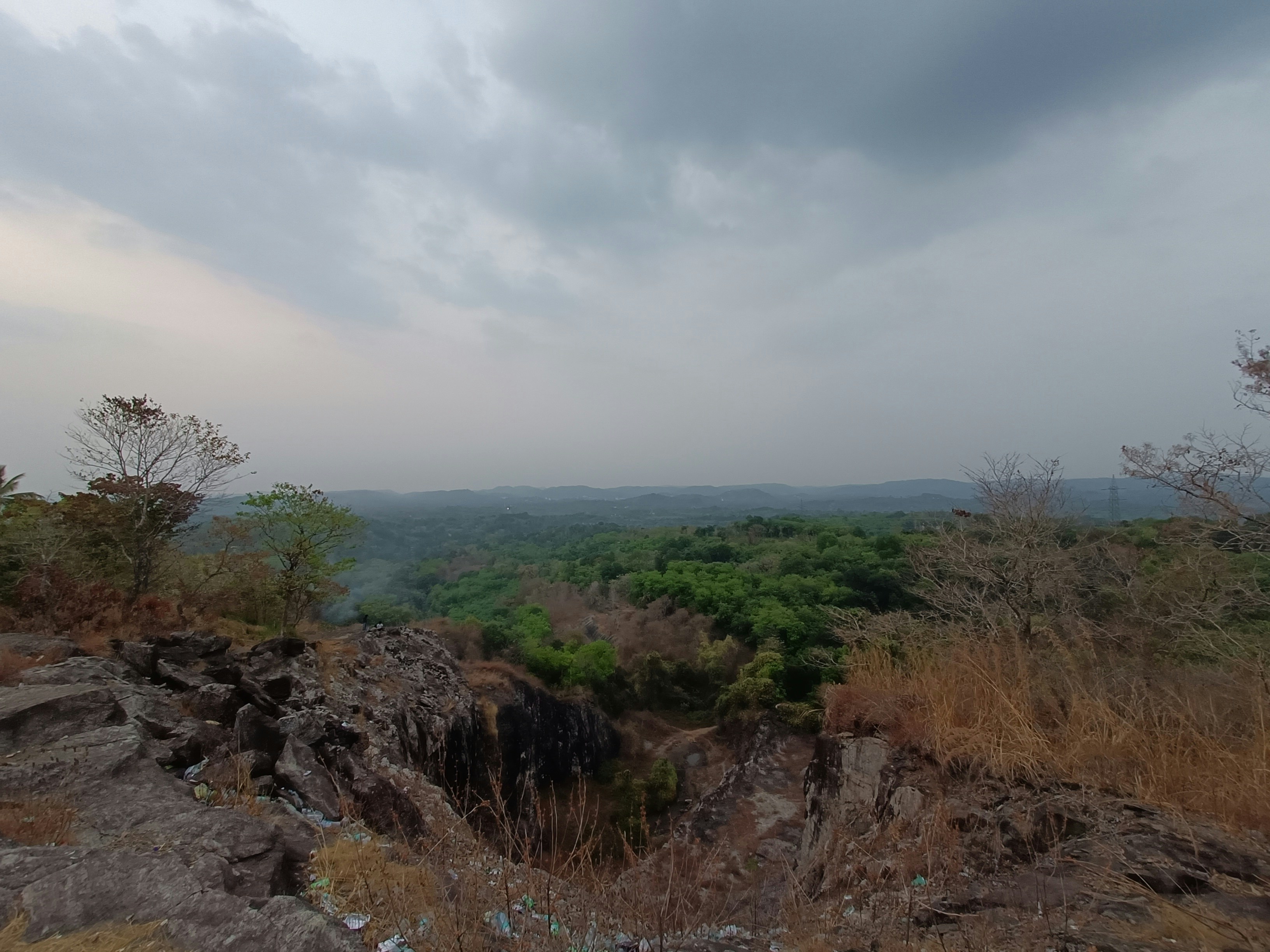 Overcast sky looms above a lush green valley and rocky foreground, suggesting an incoming storm.