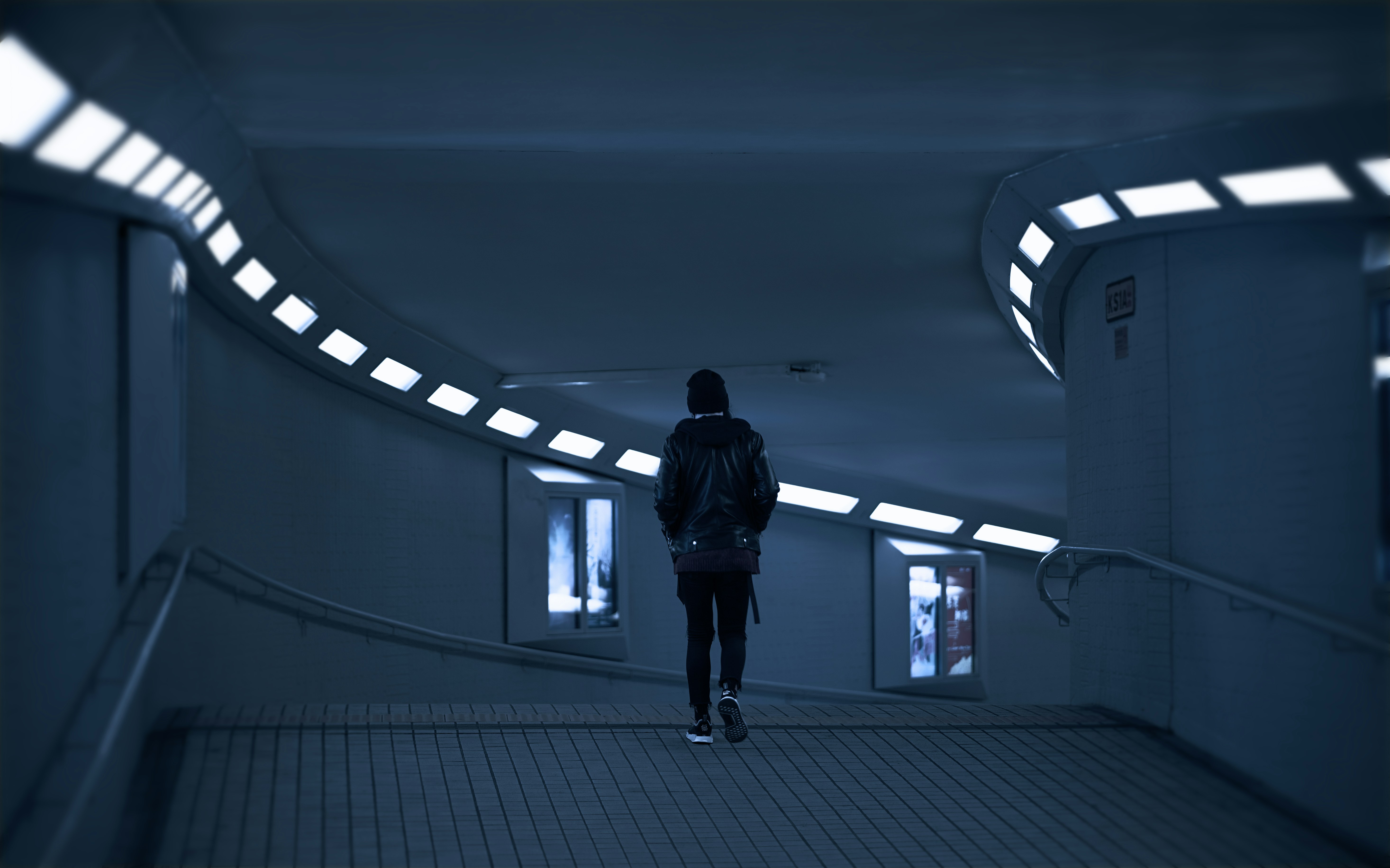 The lighting on both sides of the pedestrian tunnel is very nice, like a movie film. | a person walking down a hallway in a building