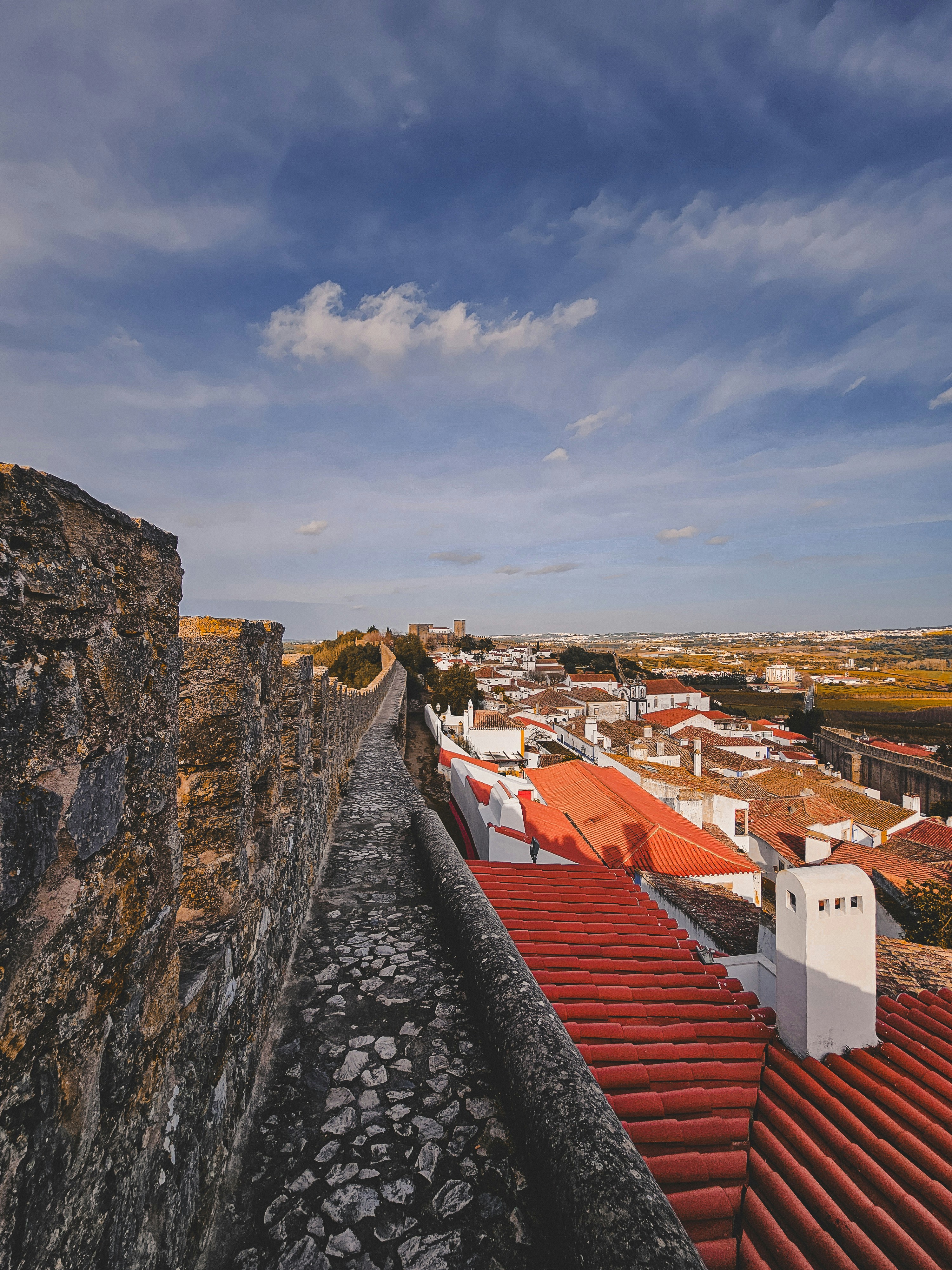 Edge of the Ramparts: Sunlit Red-Tiled Rooftops Beyond an Ancient Wall