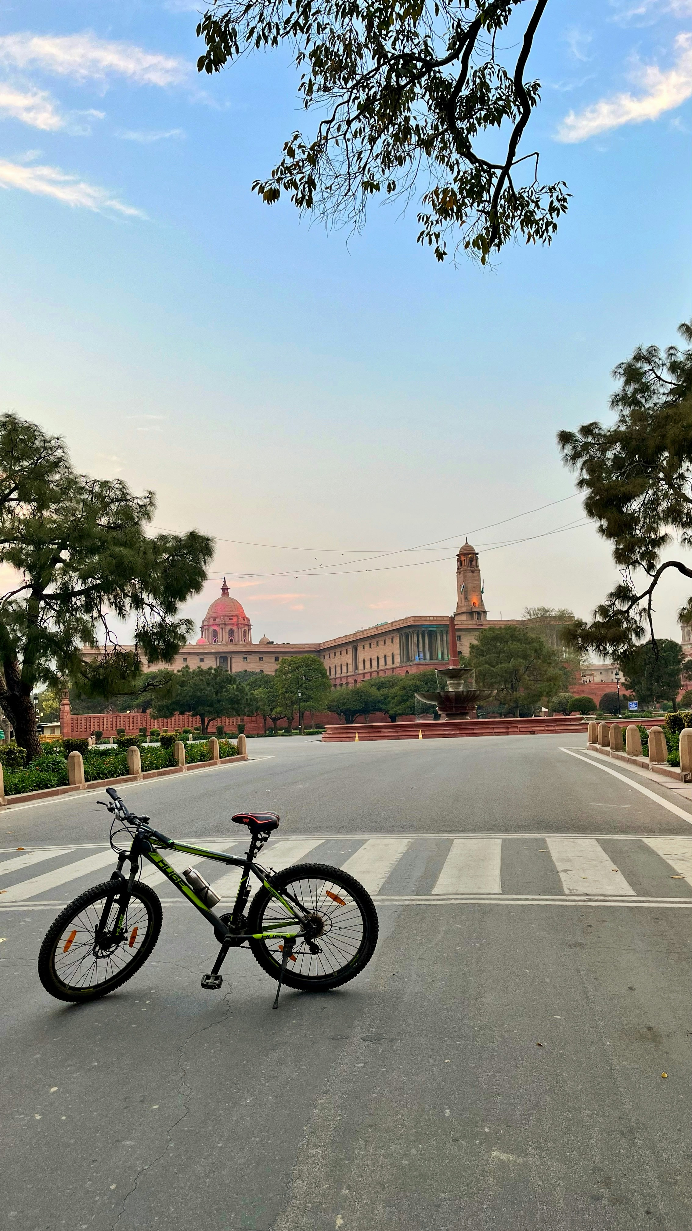 A bicycle rests on a crosswalk, framed by lush trees and a historic building in the background, showcasing a peaceful urban setting.