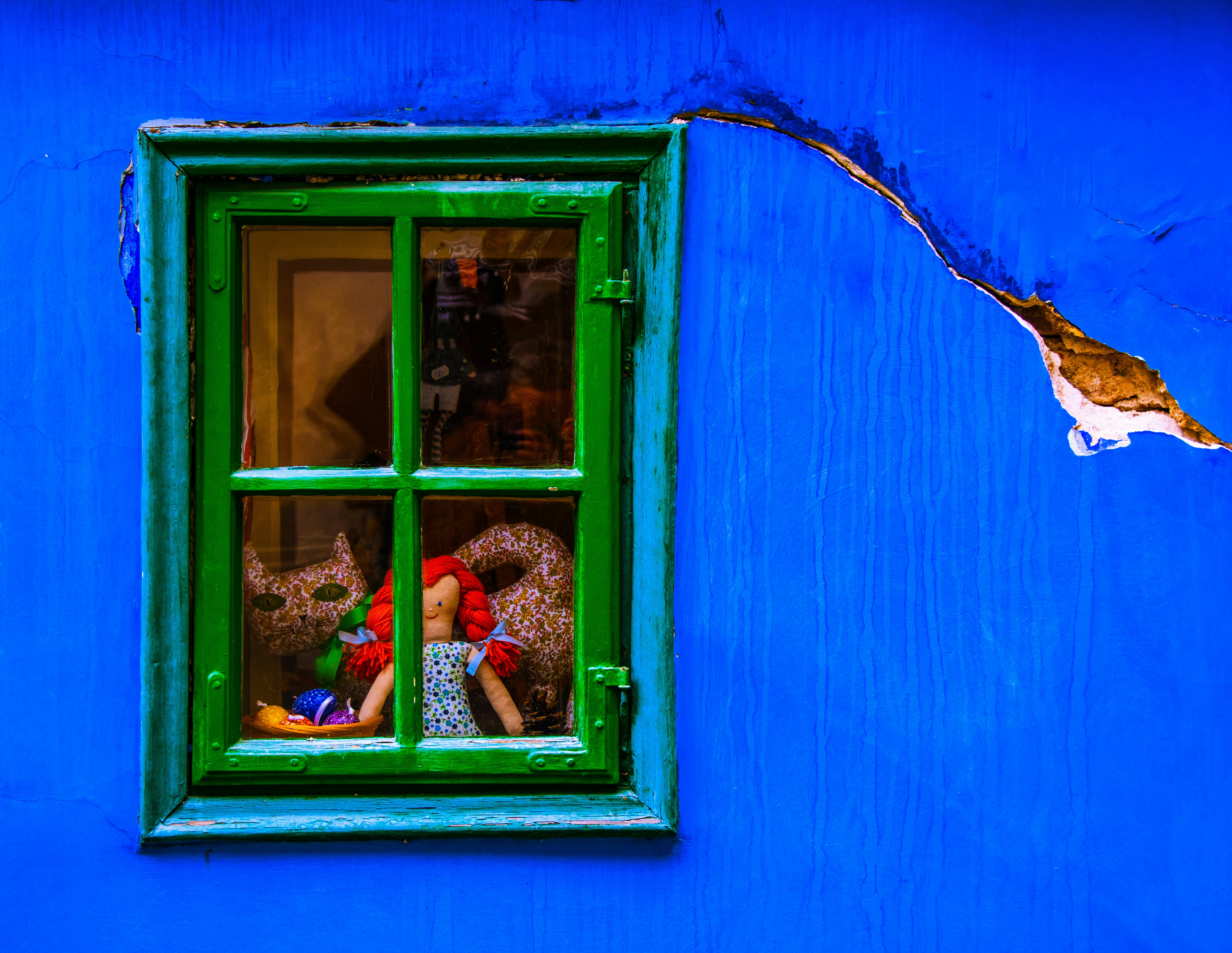 Emerald Window on a Cracked Blue Wall Reveals a Cluster of Plush Behind Four Panes
