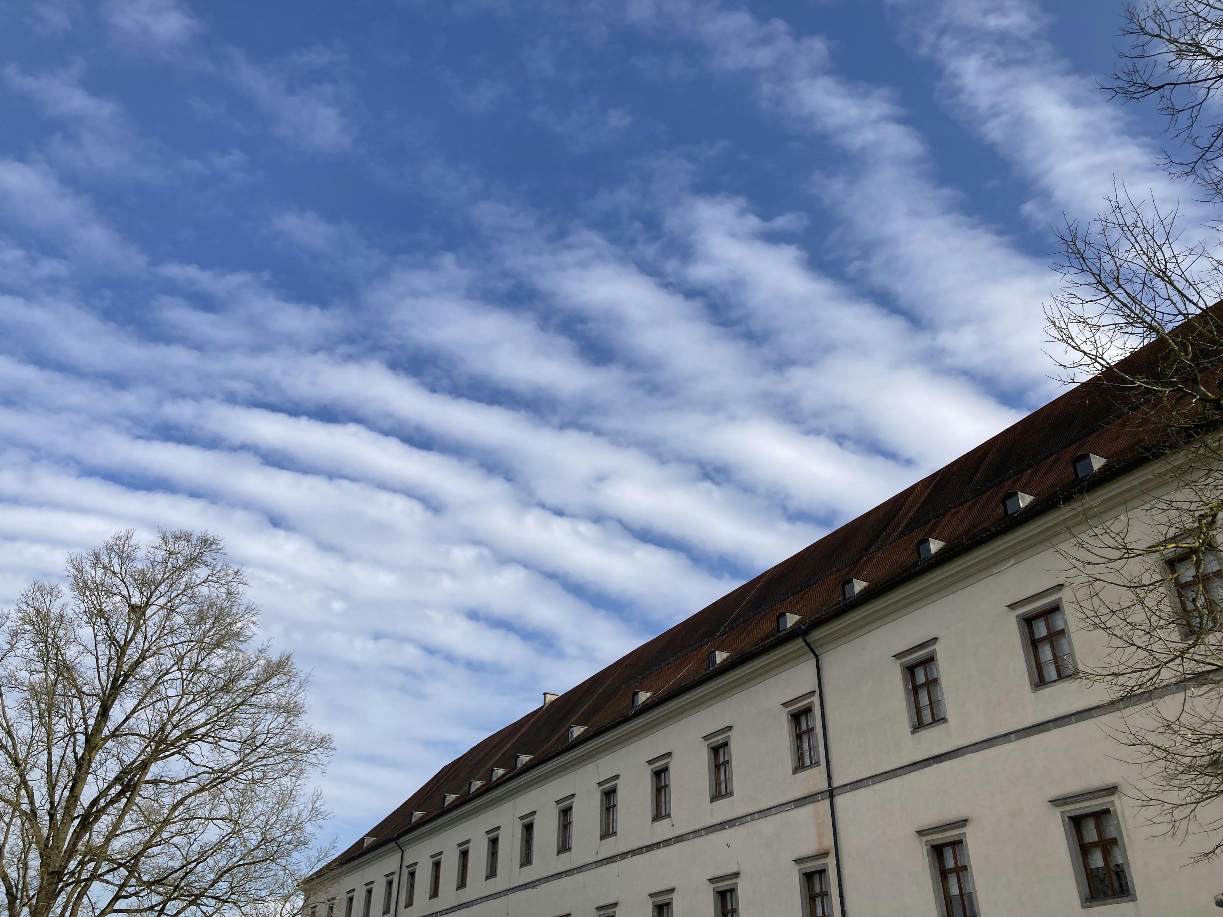 Linear clouds stretch across a bright blue sky above the Schlossmuseum's roofline in Linz, Austria.