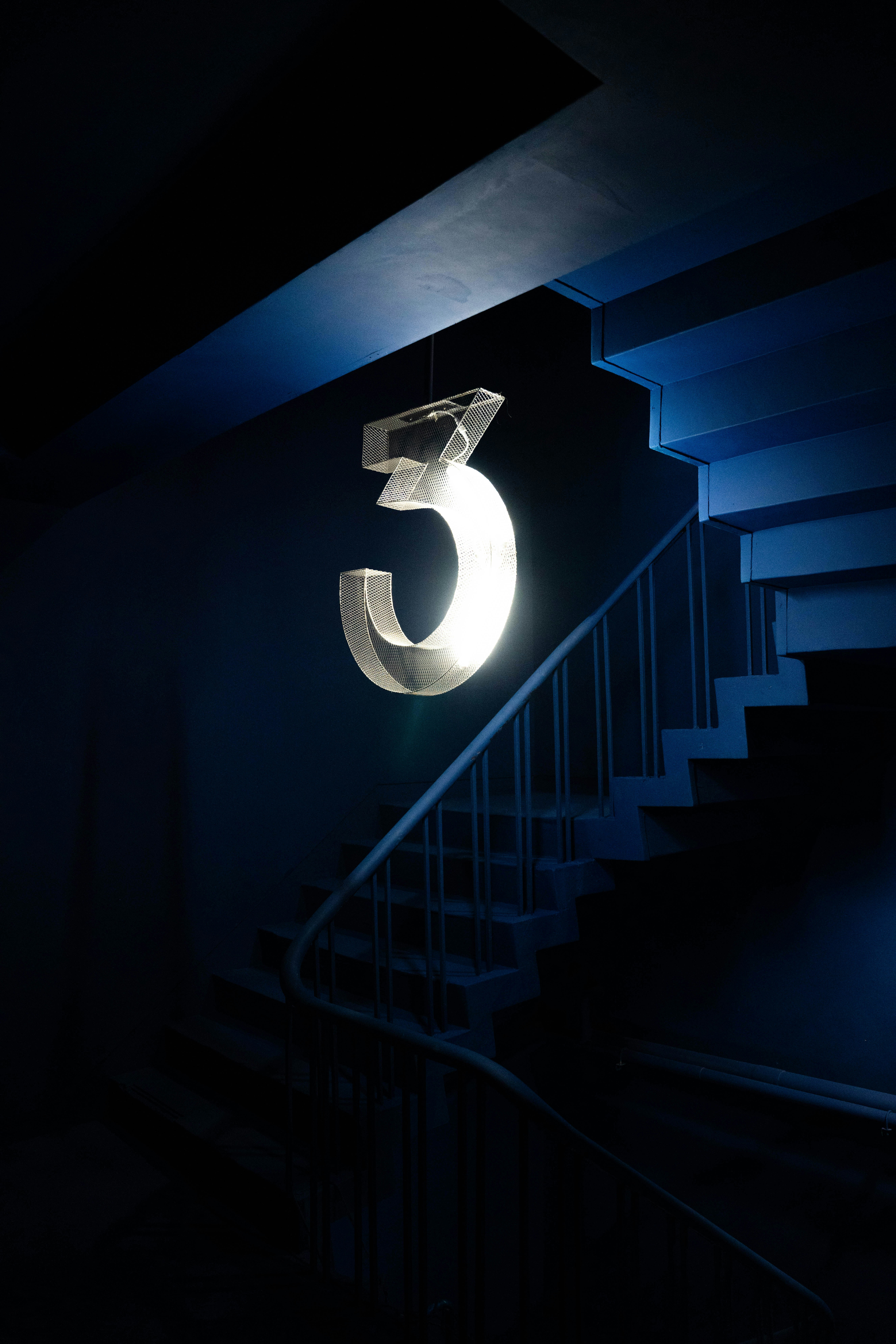 Neon Numeral Five: A Quiet Descent Through Blue Stairwell Light