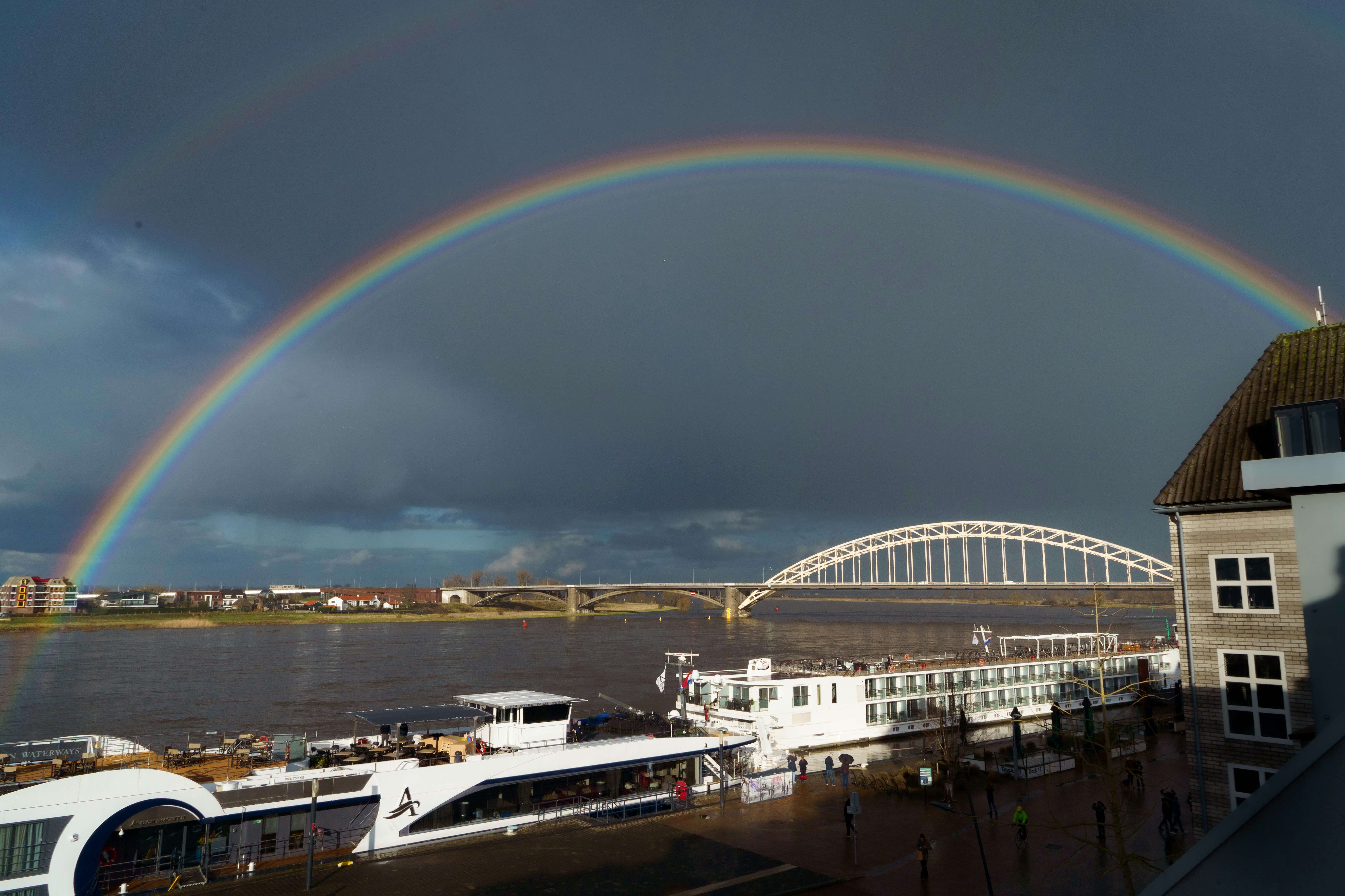 Double rainbow arches over a river, framing a bridge against a dark sky.