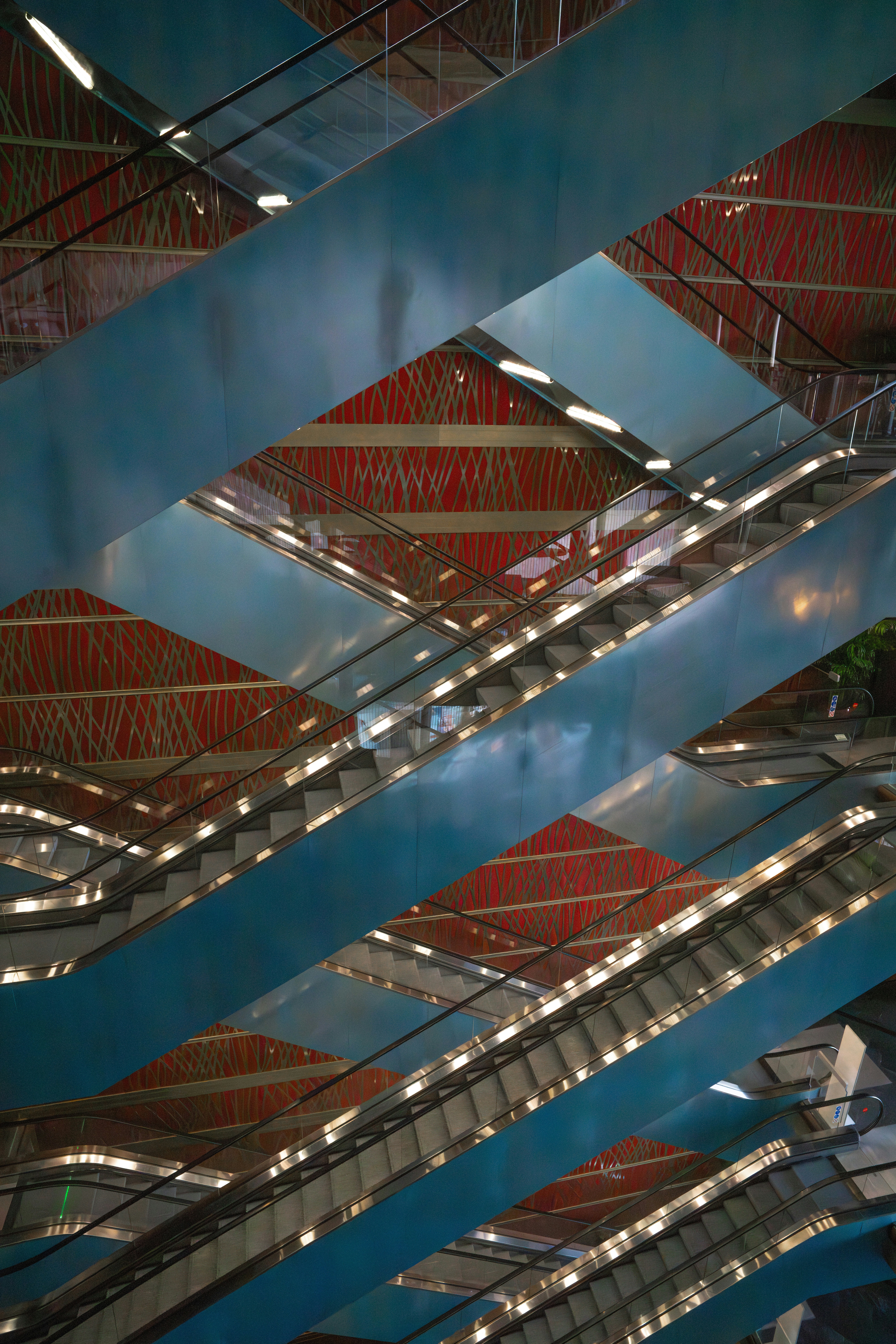 Crisscrossed Neon Ribbons: A Blue Escalator Maze in an Atrium