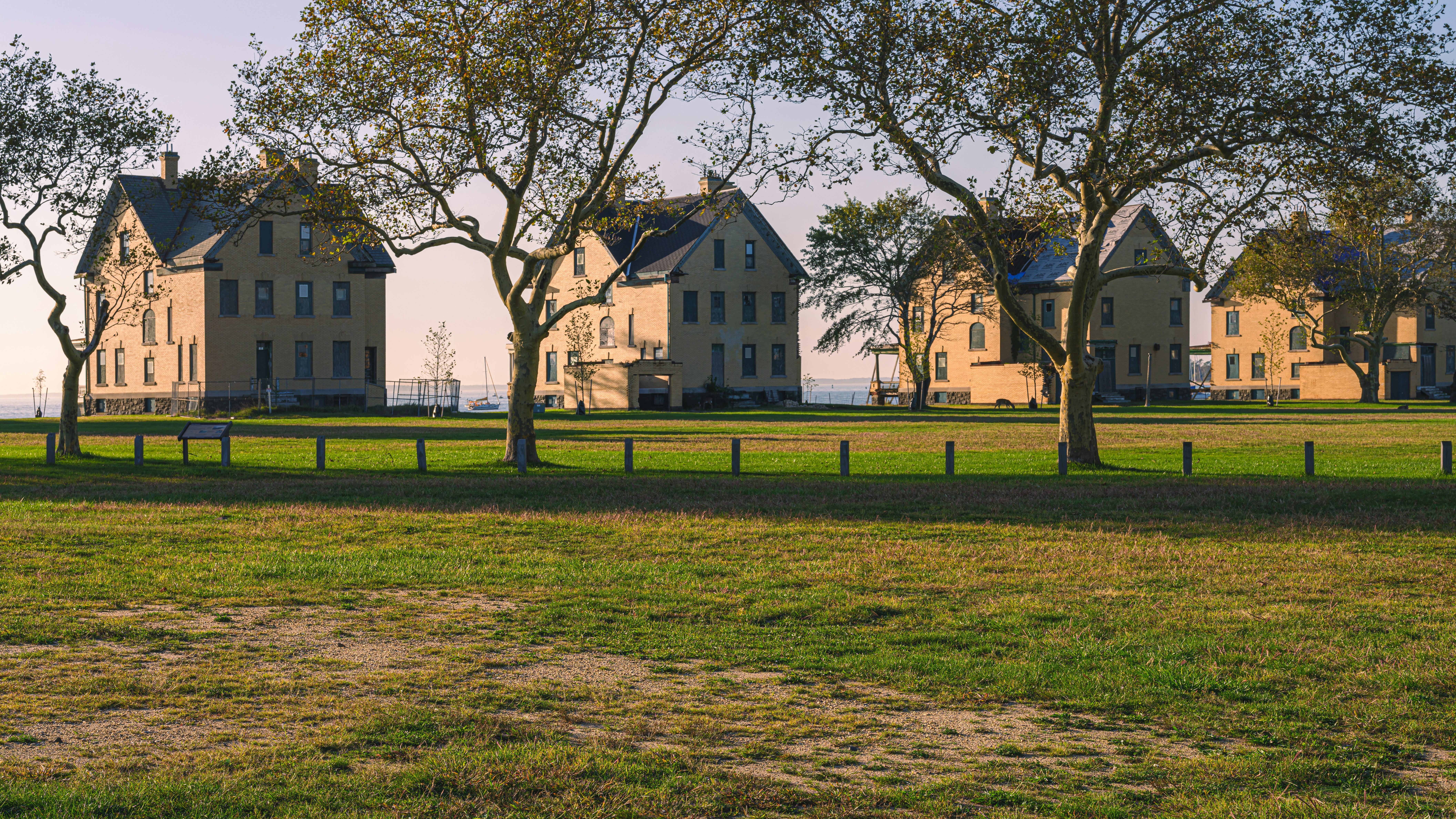 A row of vintage homesteads stands quietly against a backdrop of trees and a distant horizon, reflecting a bygone era of architecture.