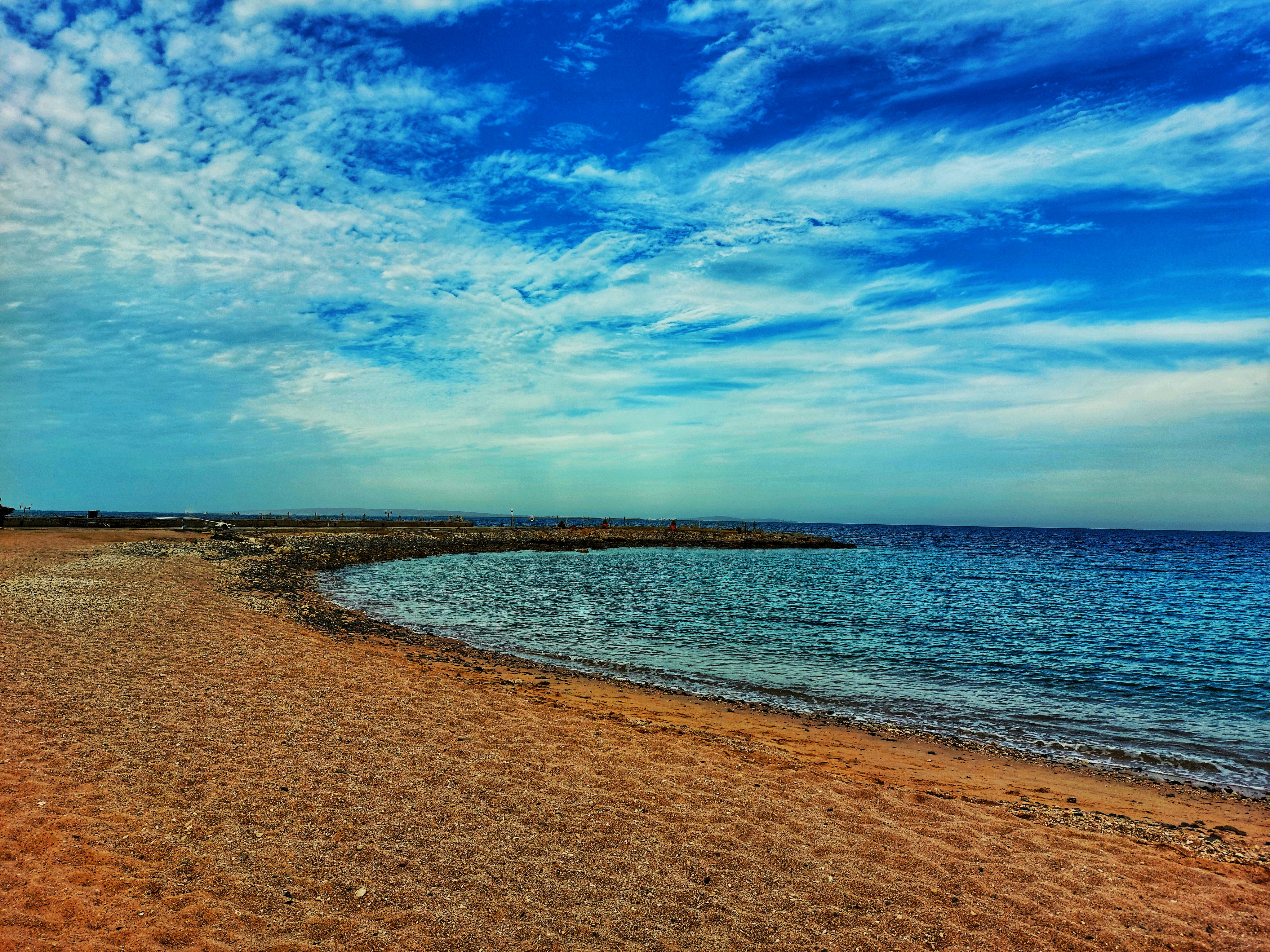 Expansive sandy beach meeting a vibrant blue sky with wispy clouds, beside a calm sea.