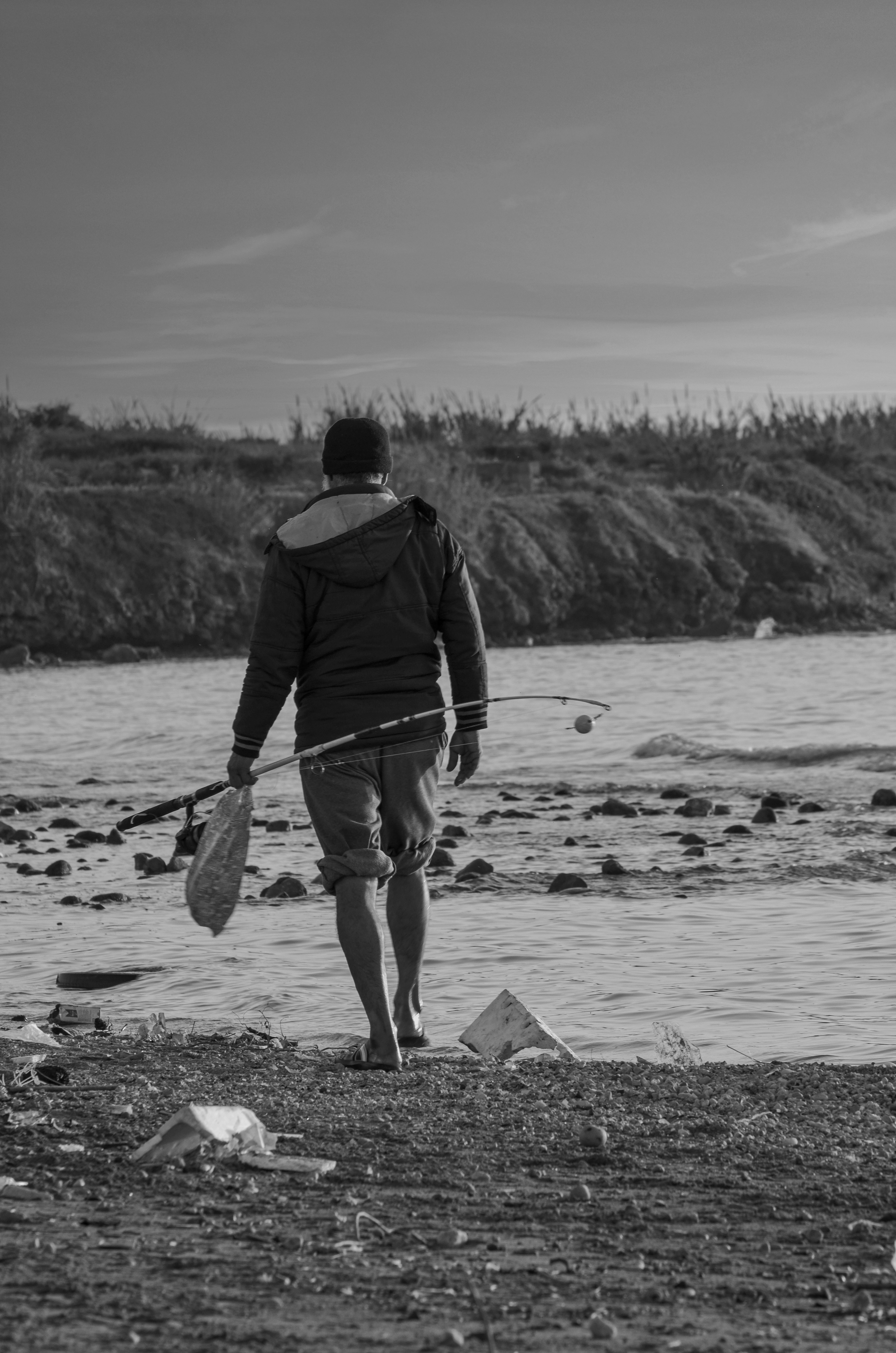 Footsteps Toward the Tide: A Lone Fisherman on a Pebble Shore