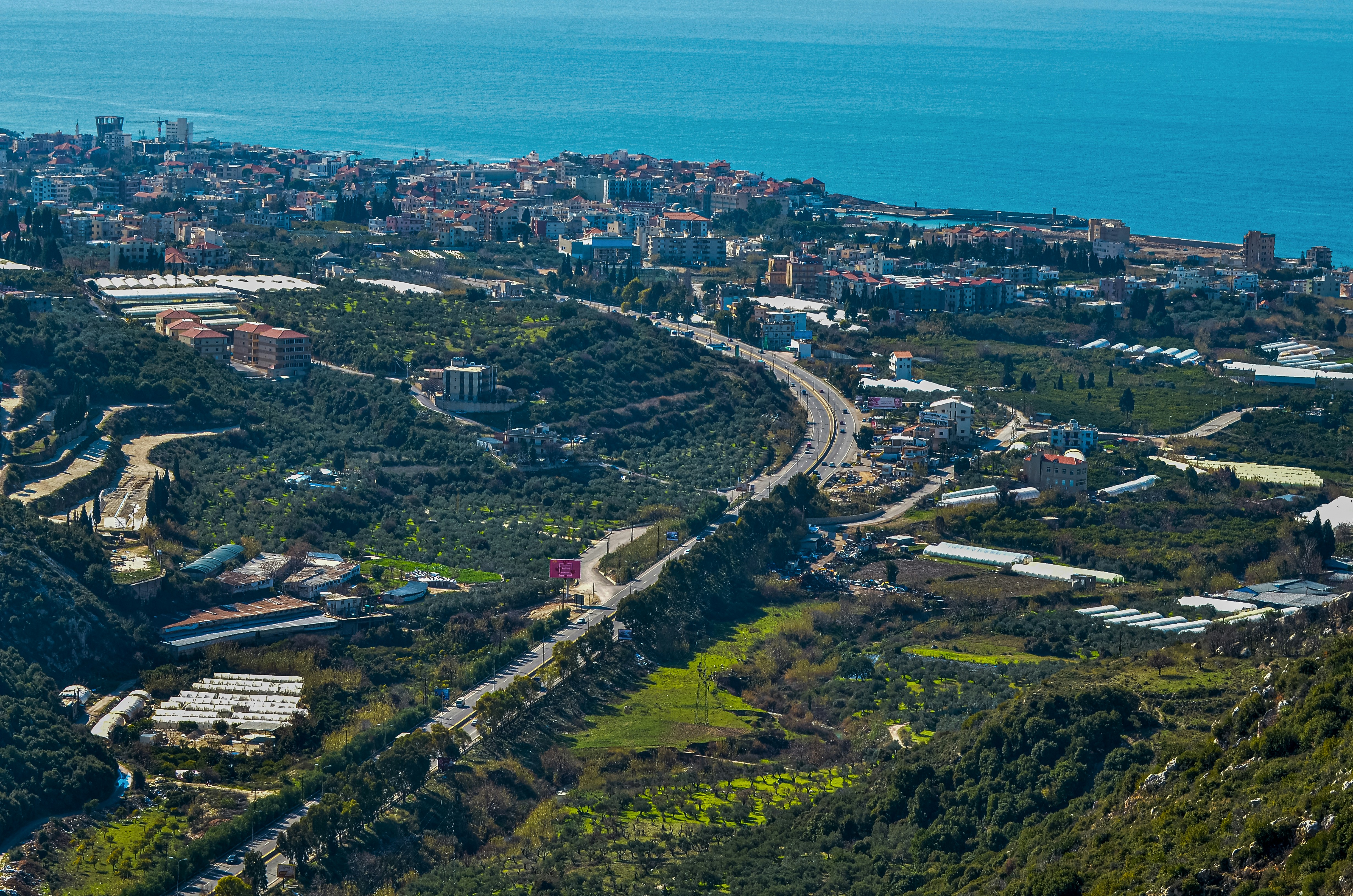 Coastal Hillside Odyssey: Aerial View of a Winding Road Through a Sea-Front Town