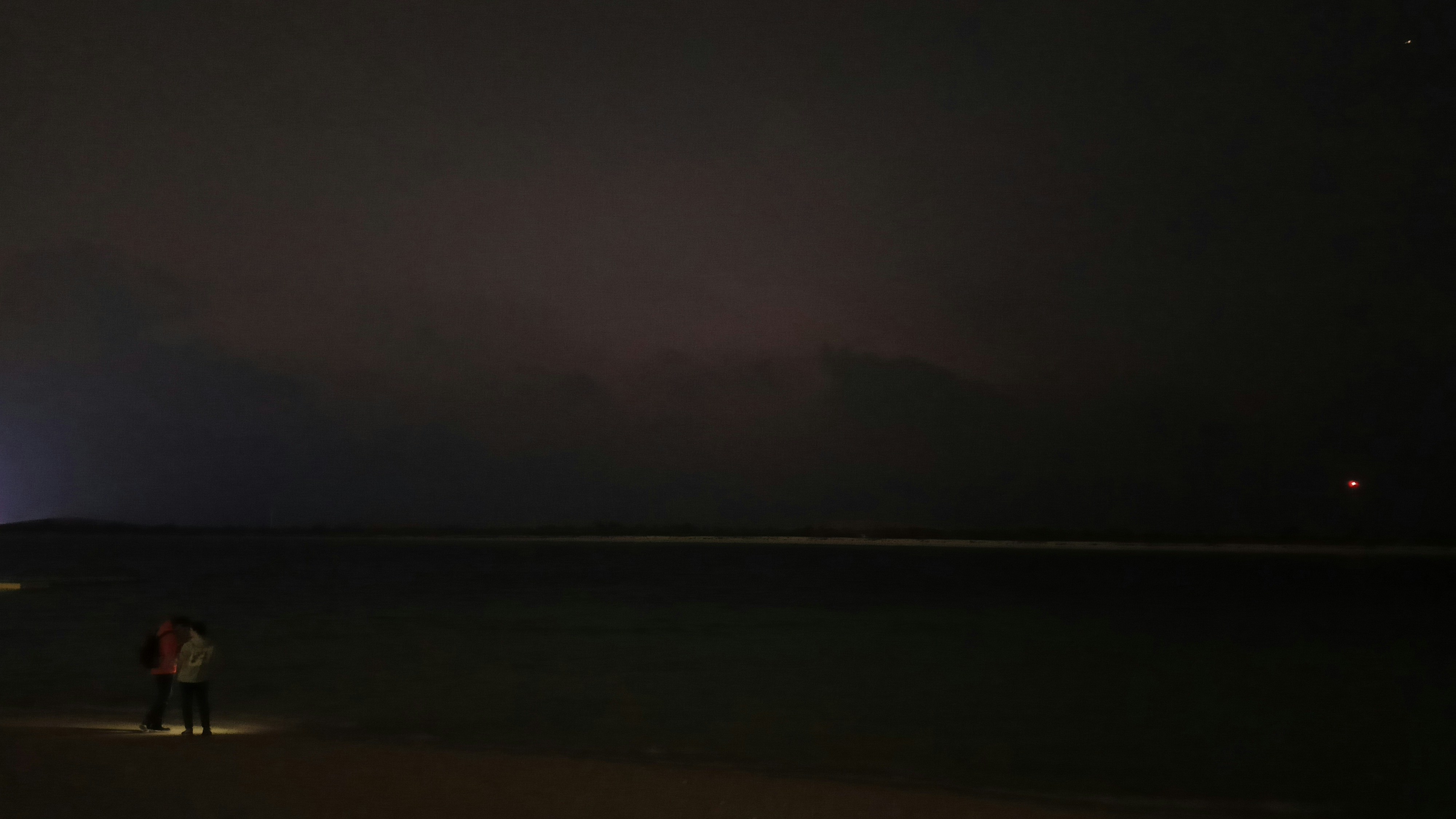 two people standing on a beach at night