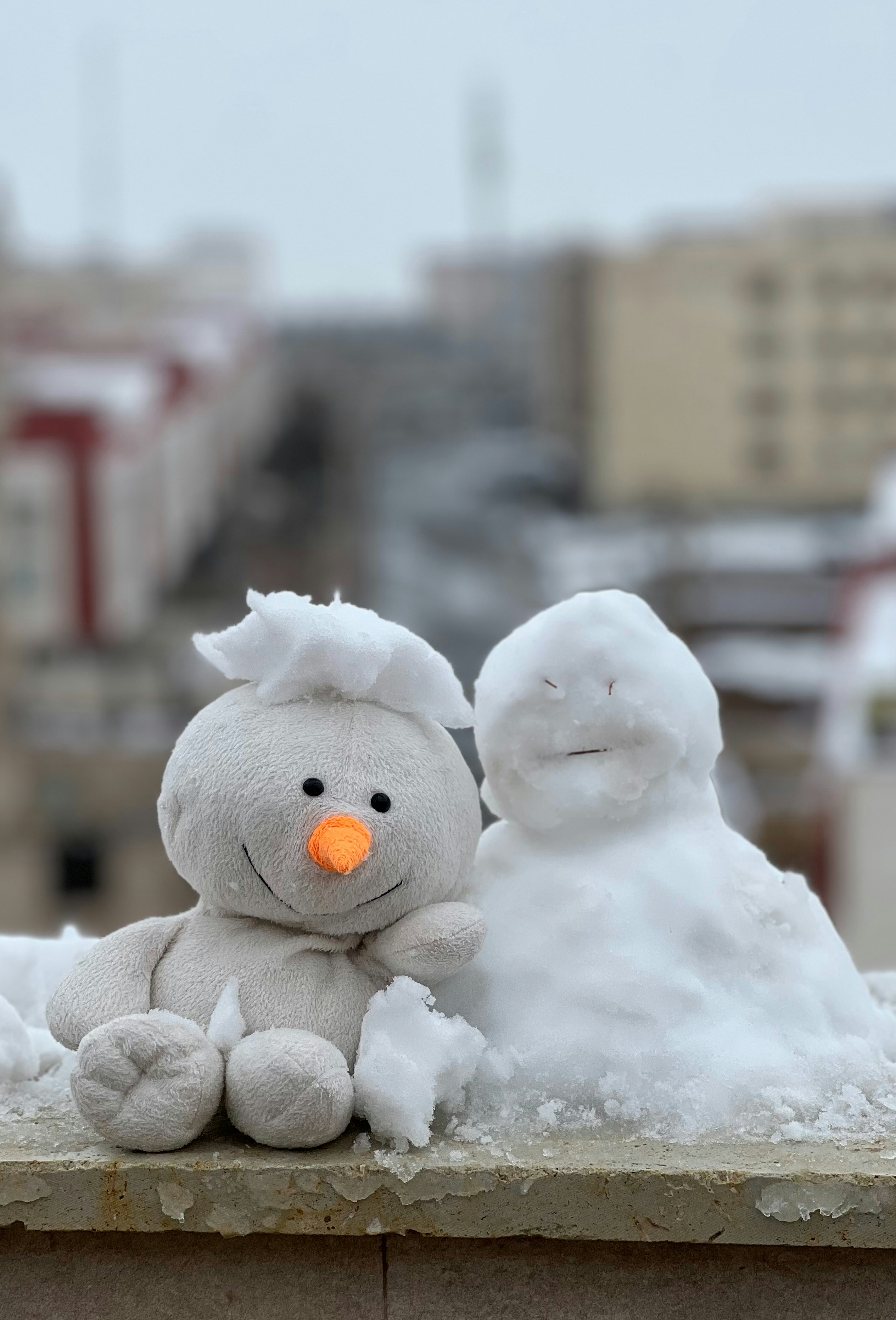 Plush Snowman on a Snow-Dusted Rooftop Against a Blurred Cityscape