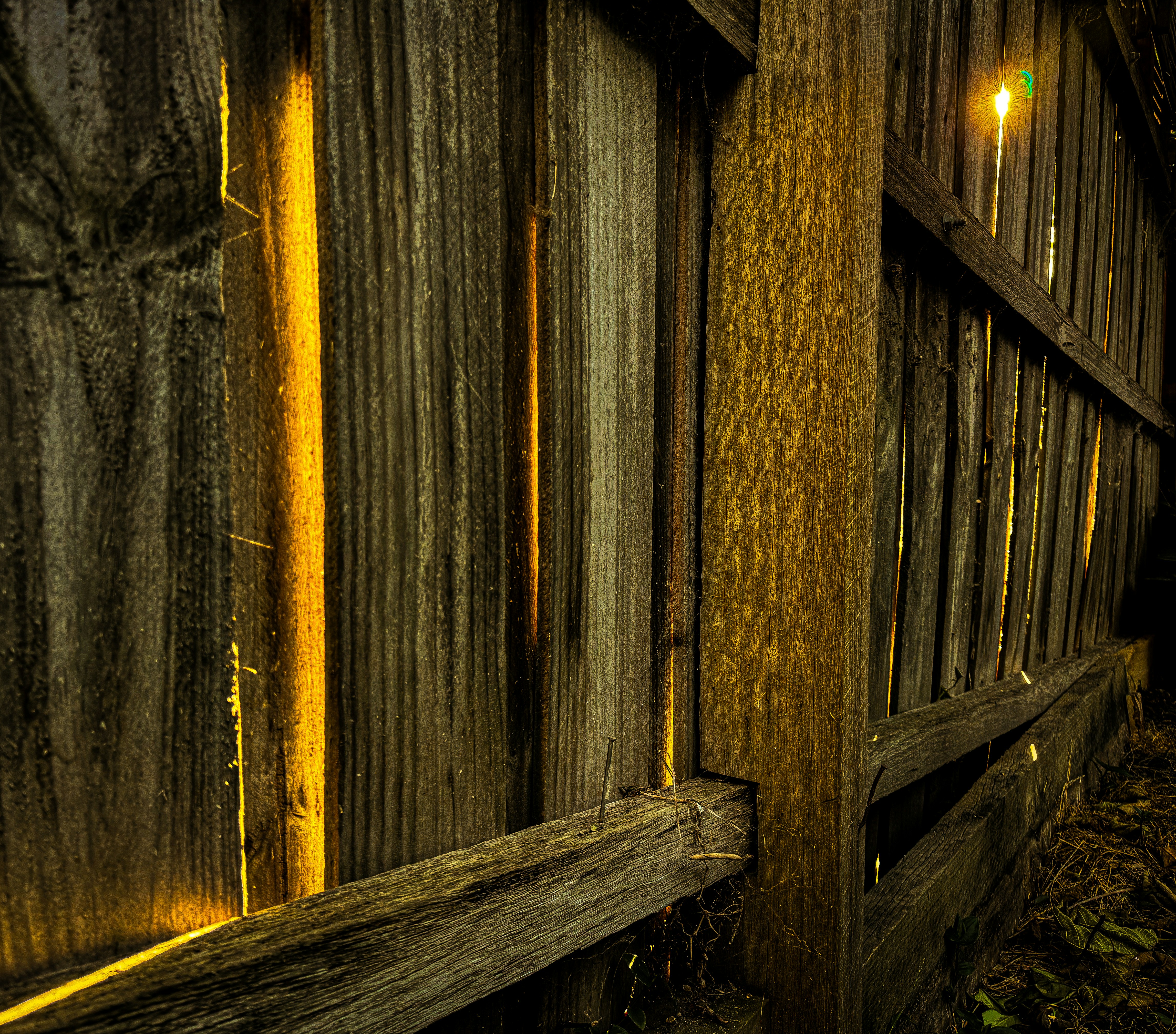 Golden light streaming through the gaps in a rustic wooden fence, highlighting the texture and age of the wood.