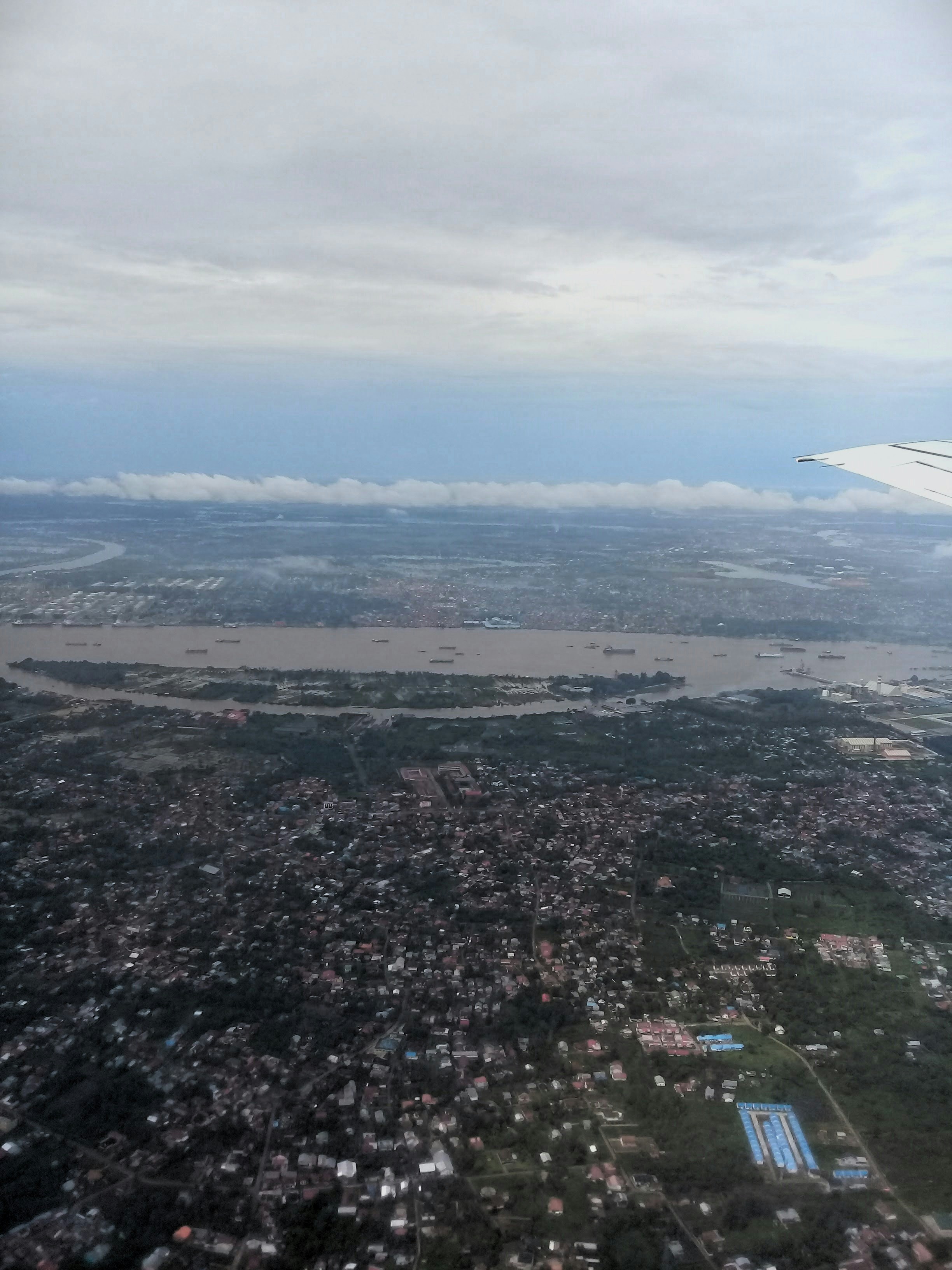 Expansive view from an airplane showcasing a winding river surrounded by urban development and greenery, with clouds hovering above. 