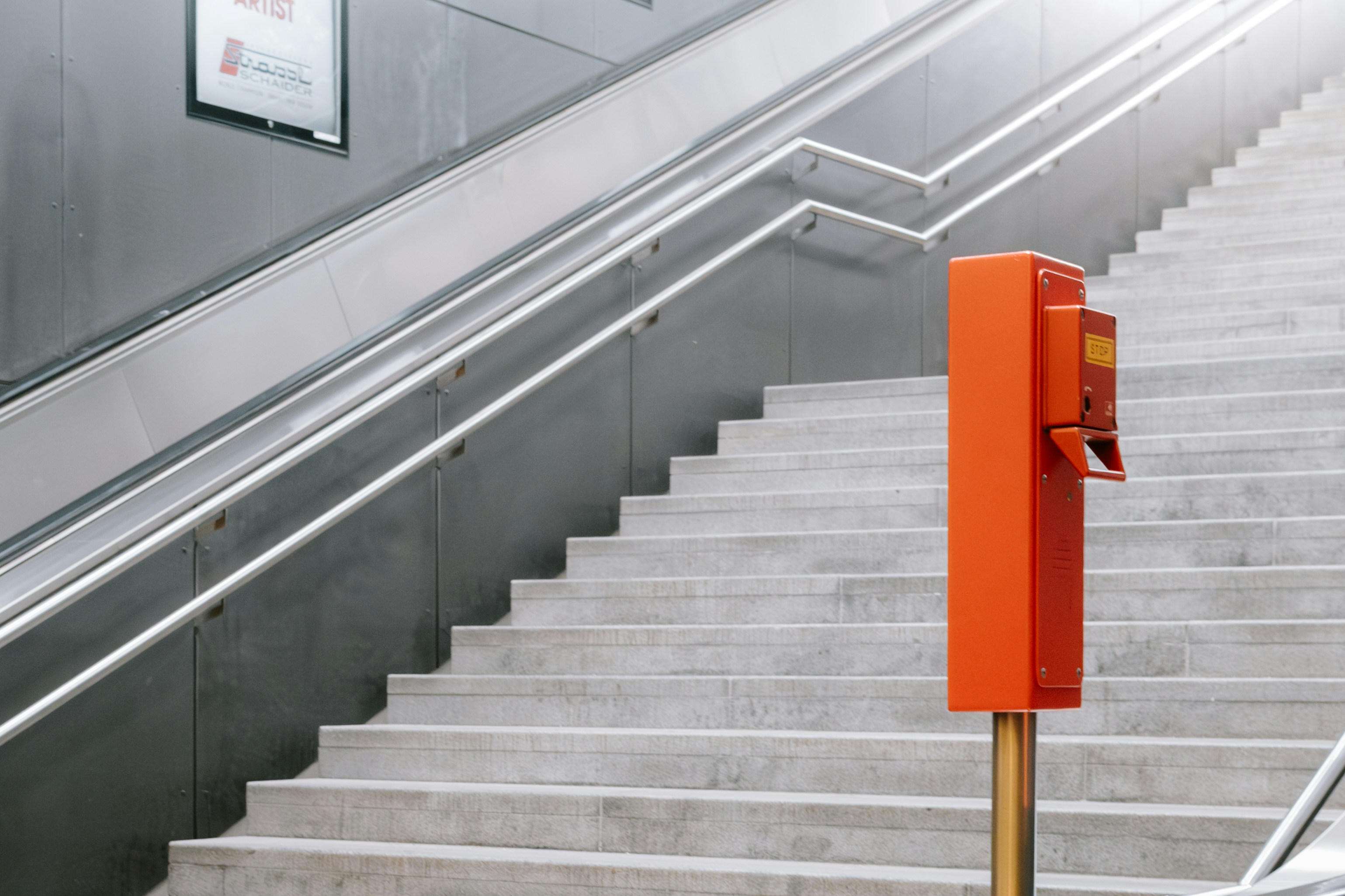 Orange Sentinel by the Stairs: A Pop of Color in Concrete Geometry