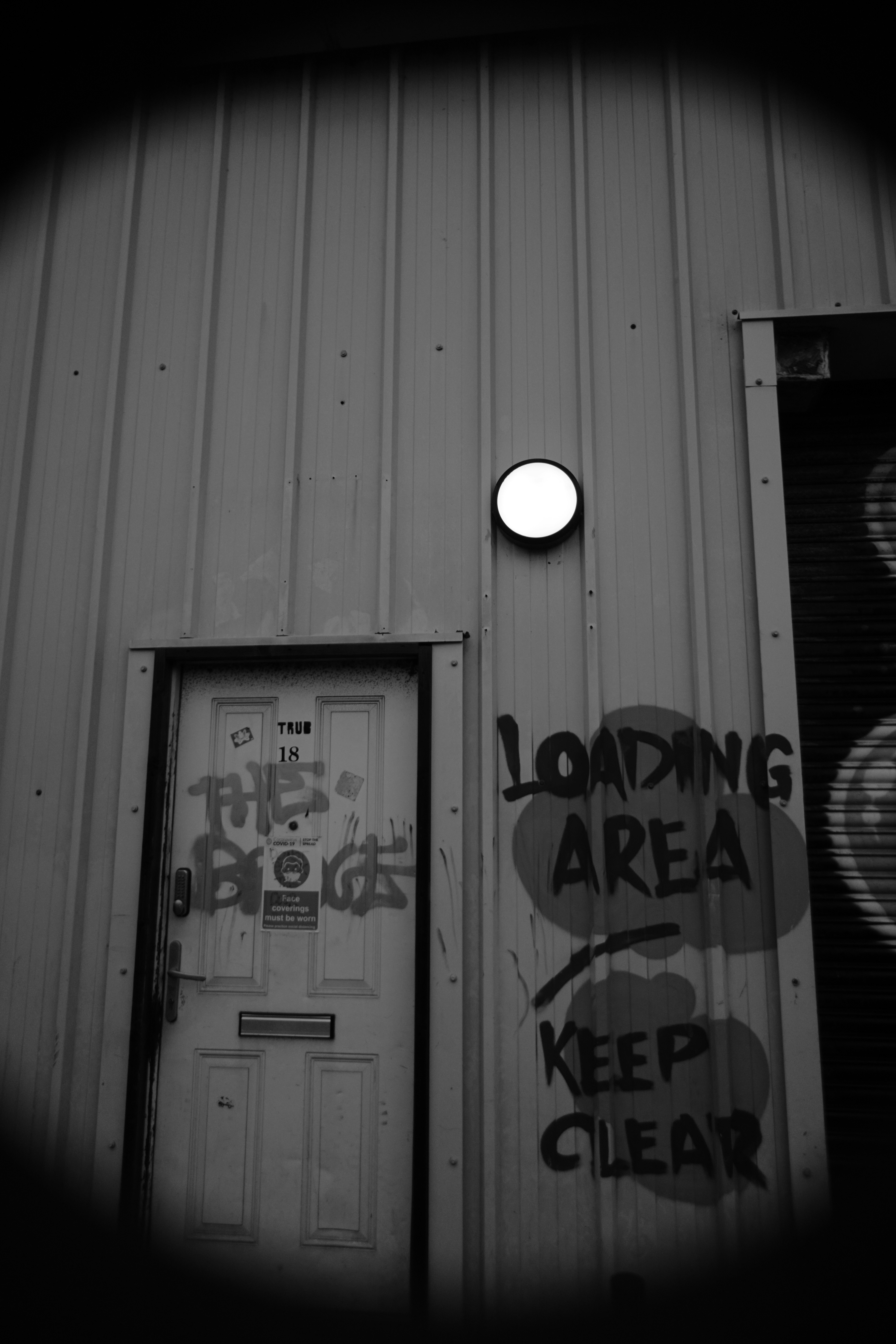 Black-and-white loading area: graffiti, door, and circular light under a vignette