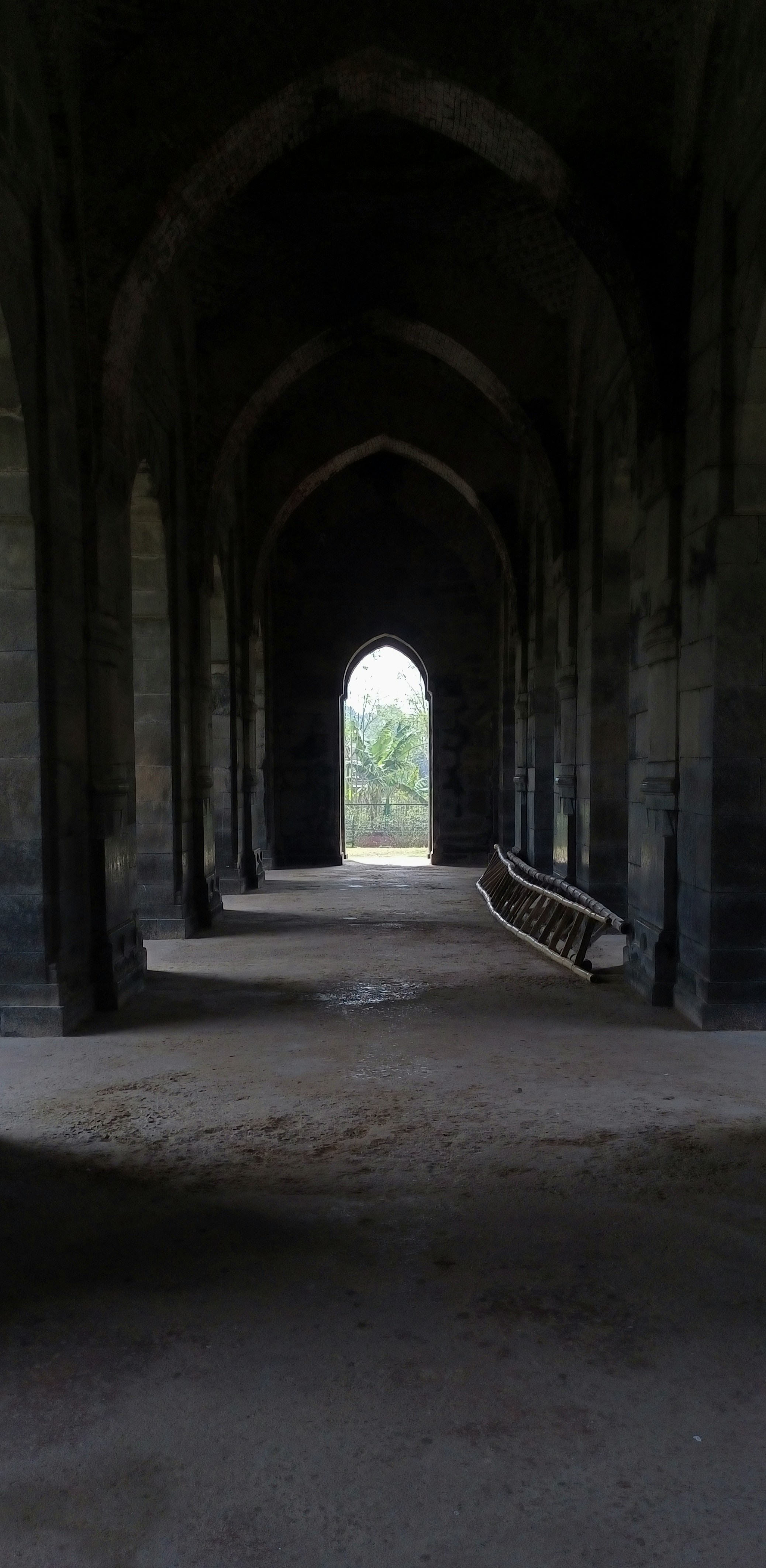 A dim stone corridor of vaulted arches extends toward a bright arched doorway at the far end.